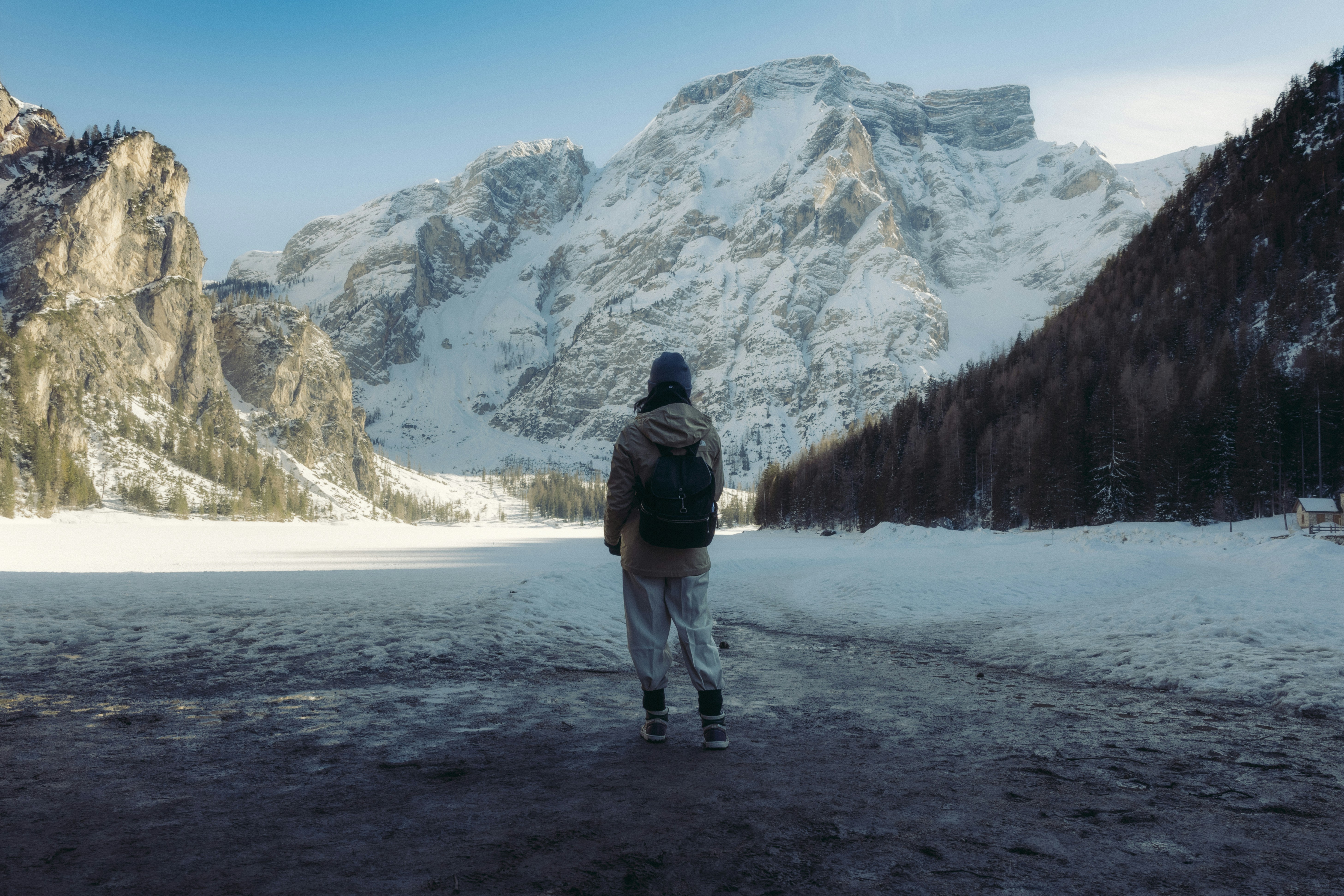 Person walking towards towering snow-covered mountains under a bright blue sky.