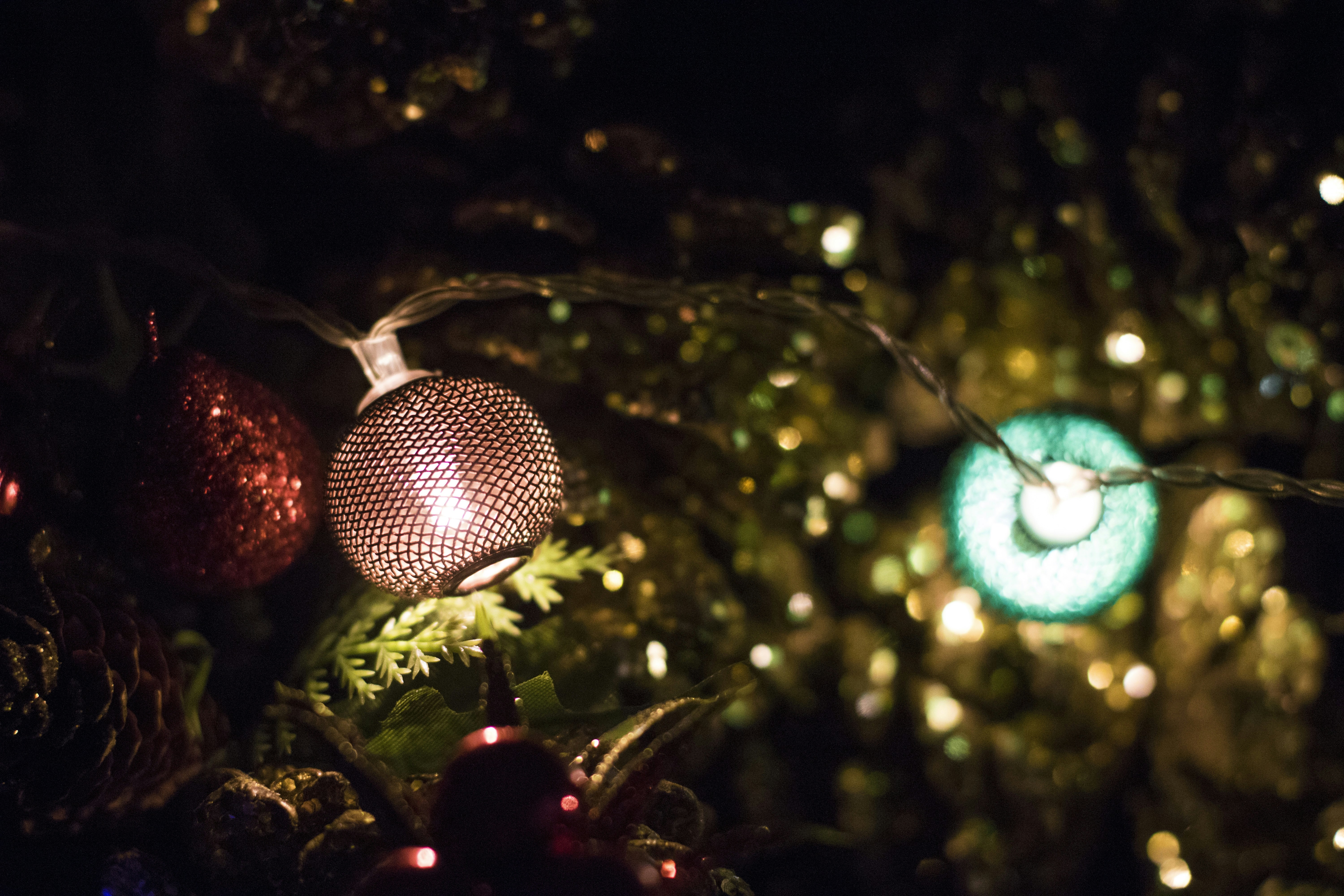 Ornamental lights and baubles on a Christmas tree, softly illuminated against a dark backdrop.