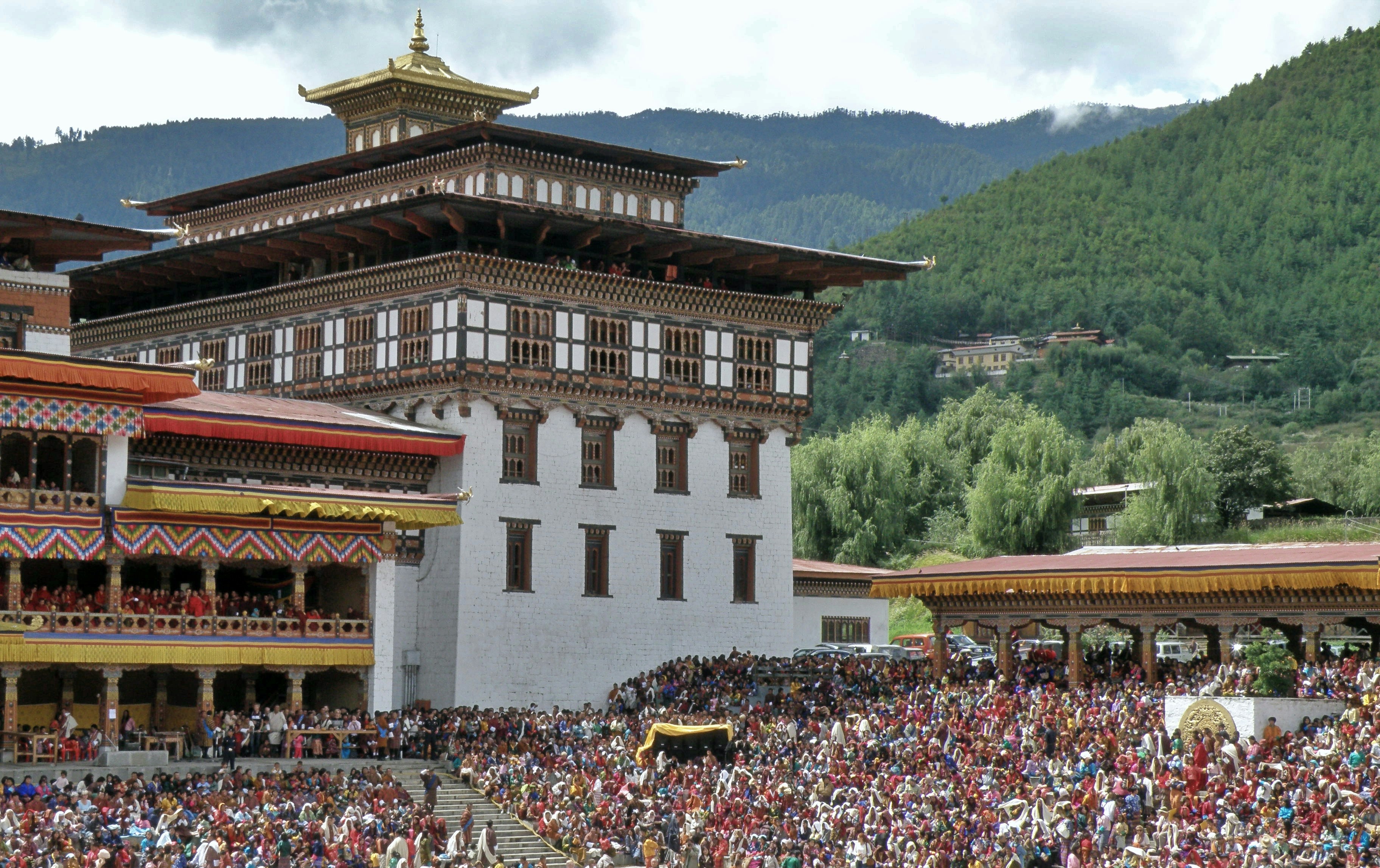 Large crowd gathered in front of a traditional Bhutanese dzong with mountains in the background.