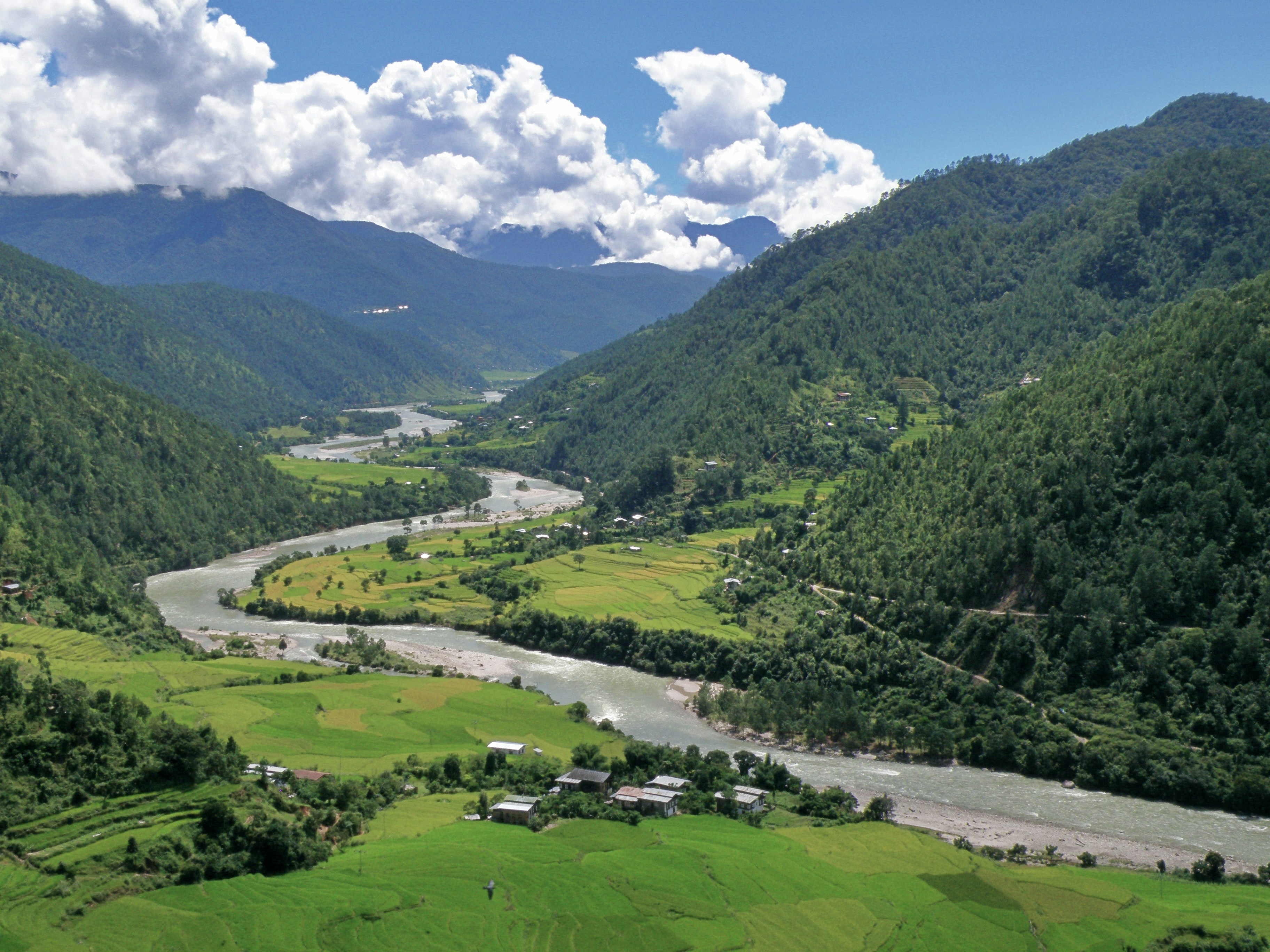 Winding river cutting through lush green valleys beneath a sky dotted with fluffy clouds.