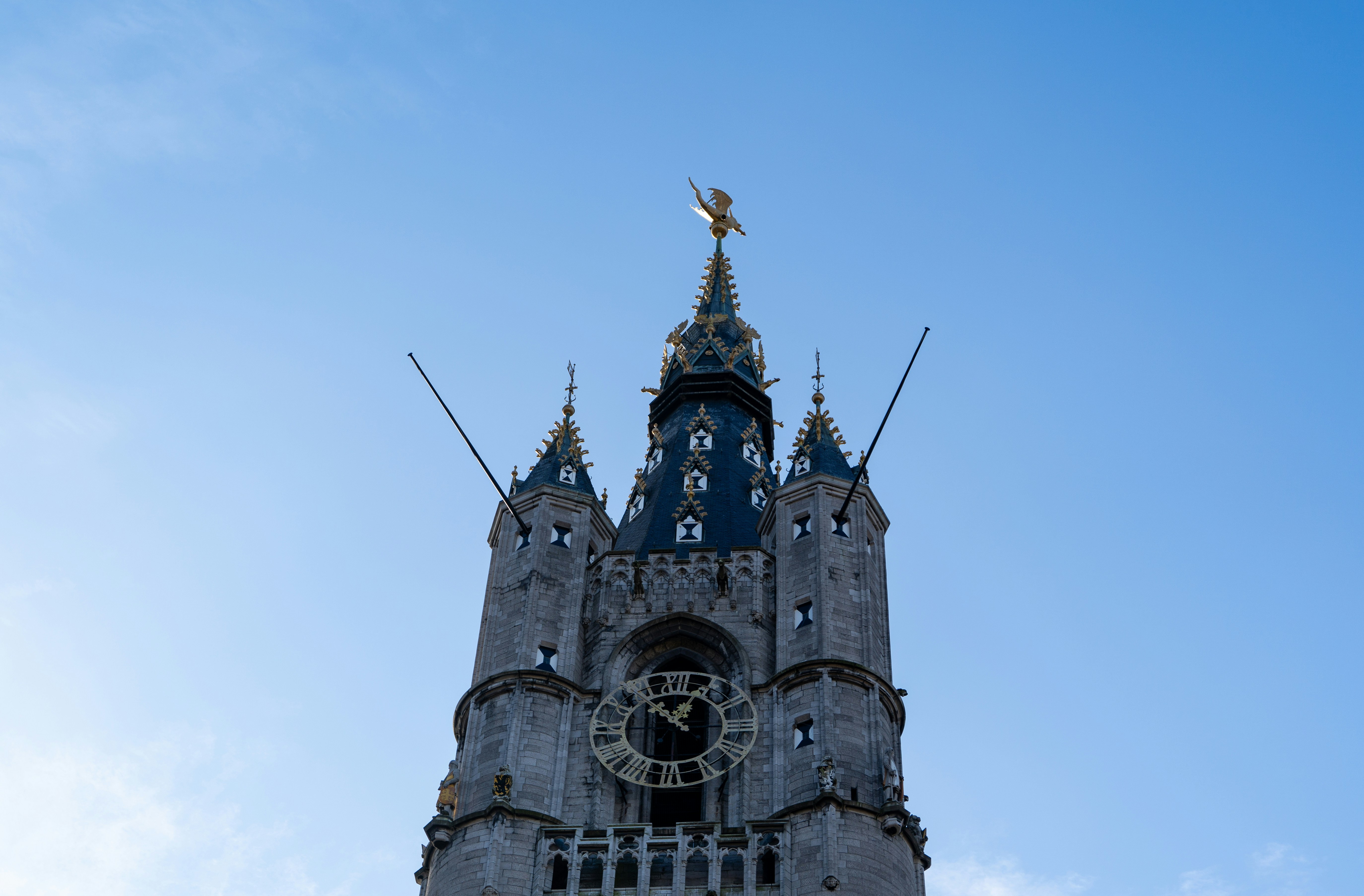 Gothic clock tower with detailed spire set against a clear blue sky.