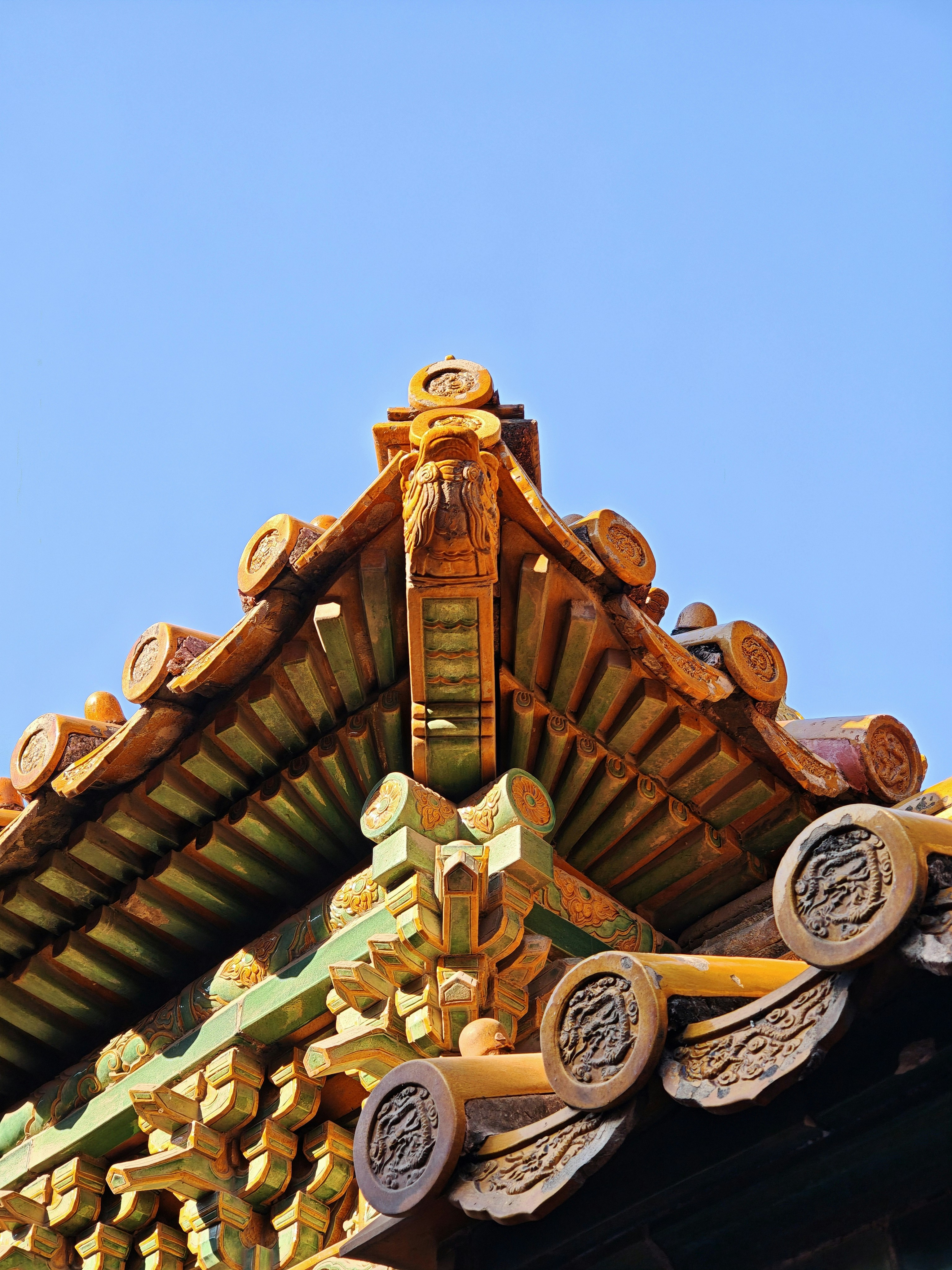 Ornately painted temple roof eaves with carved beams and circular medallions rise against a clear blue sky.
