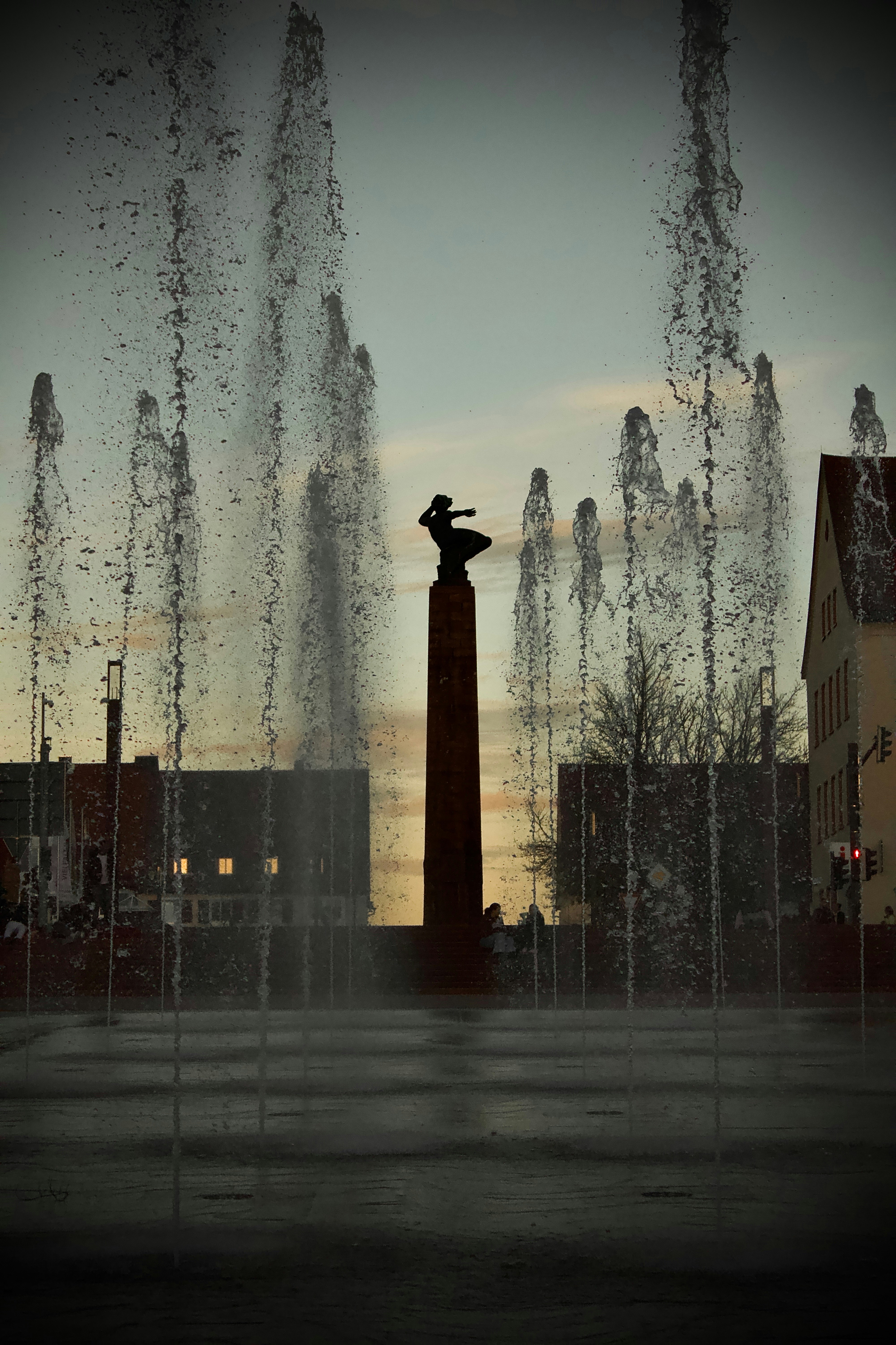 Dusk in the Square: The Statue Surrounded by Arcing Fountain Jets