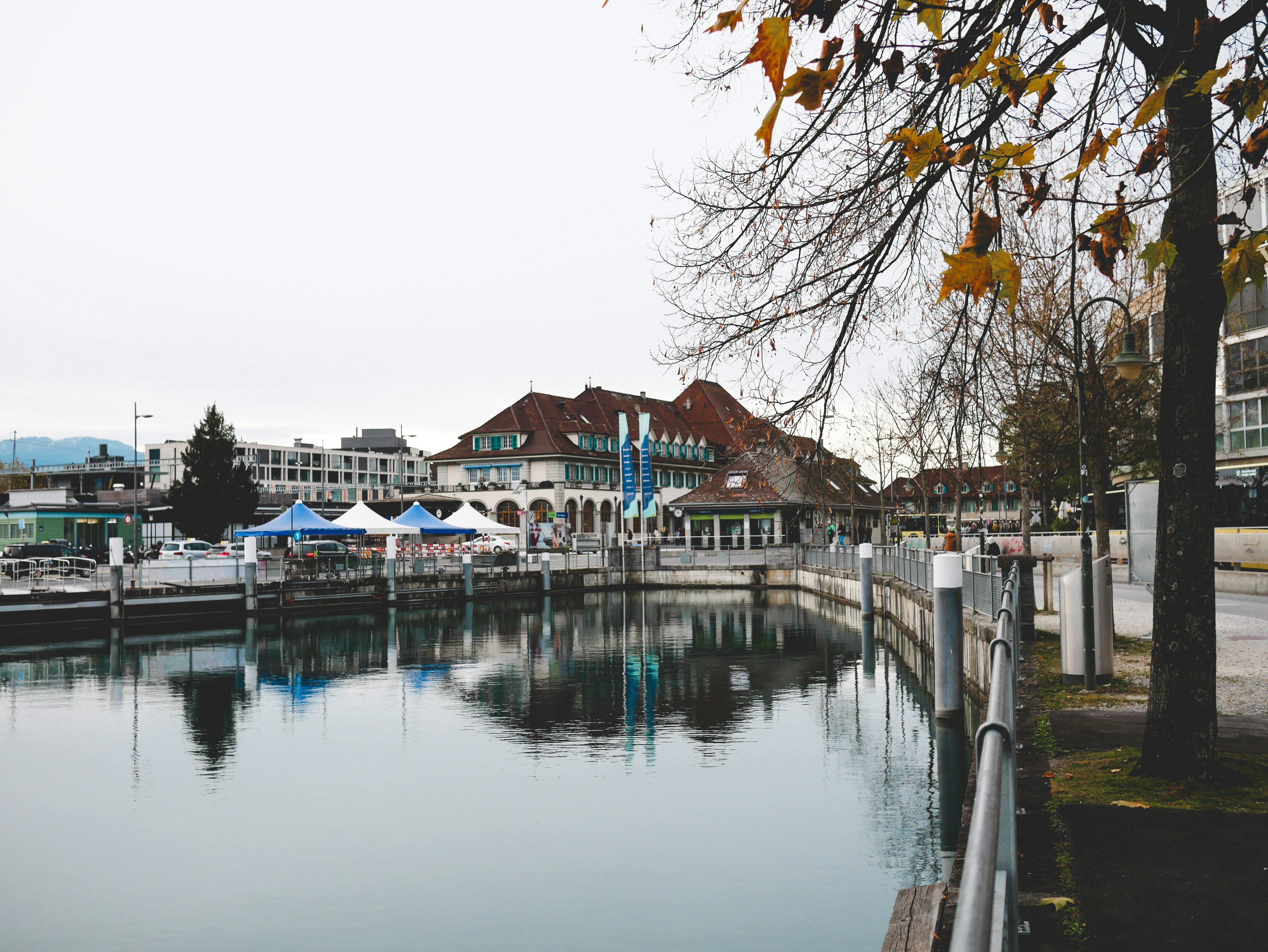 Quaint lakeside structure surrounded by serene waters, with autumn leaves framing the scene. The reflection in the water adds depth to the tranquil atmosphere.