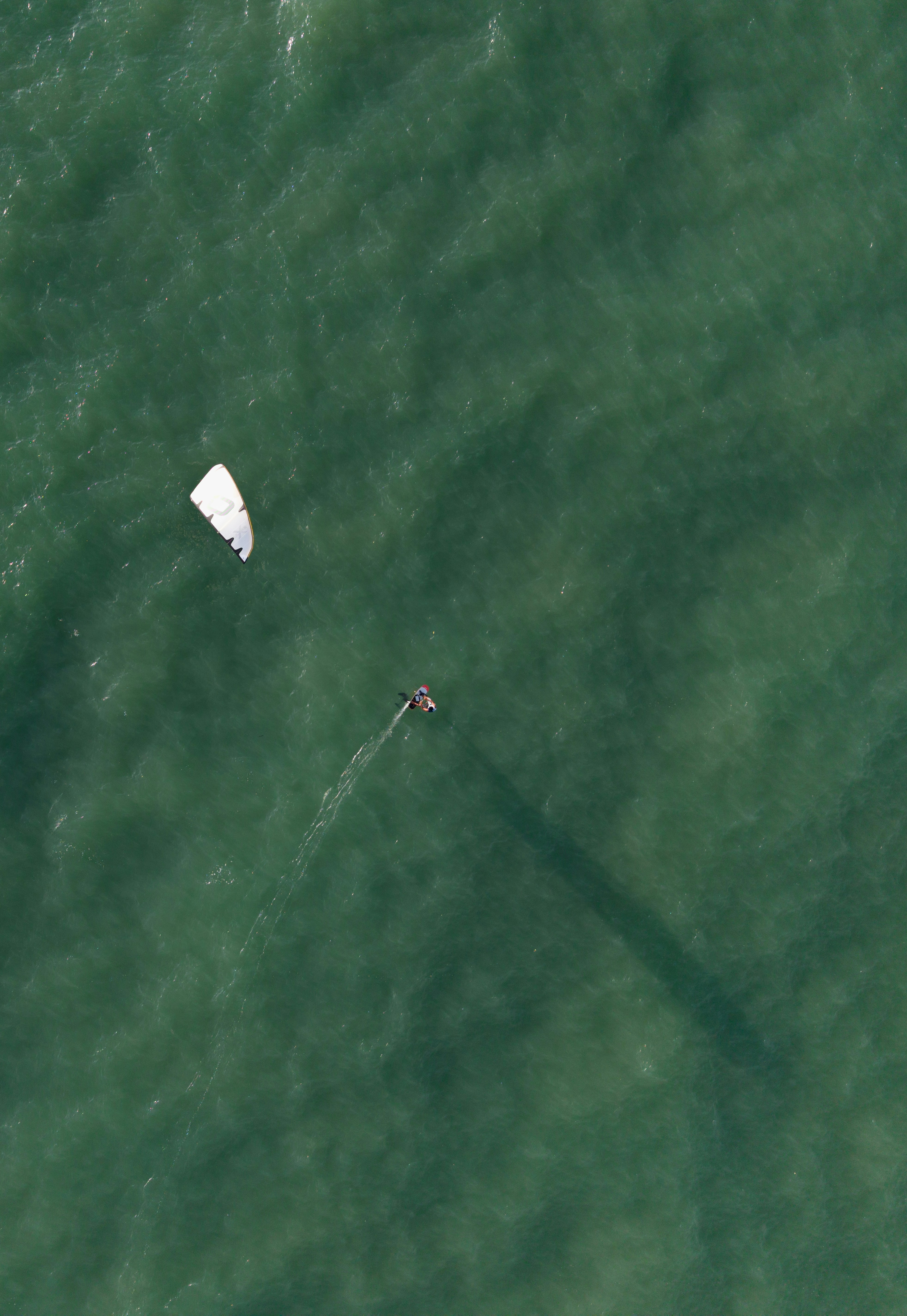 Windward Link: A lone kiteboarder traces a silver wake across emerald seas