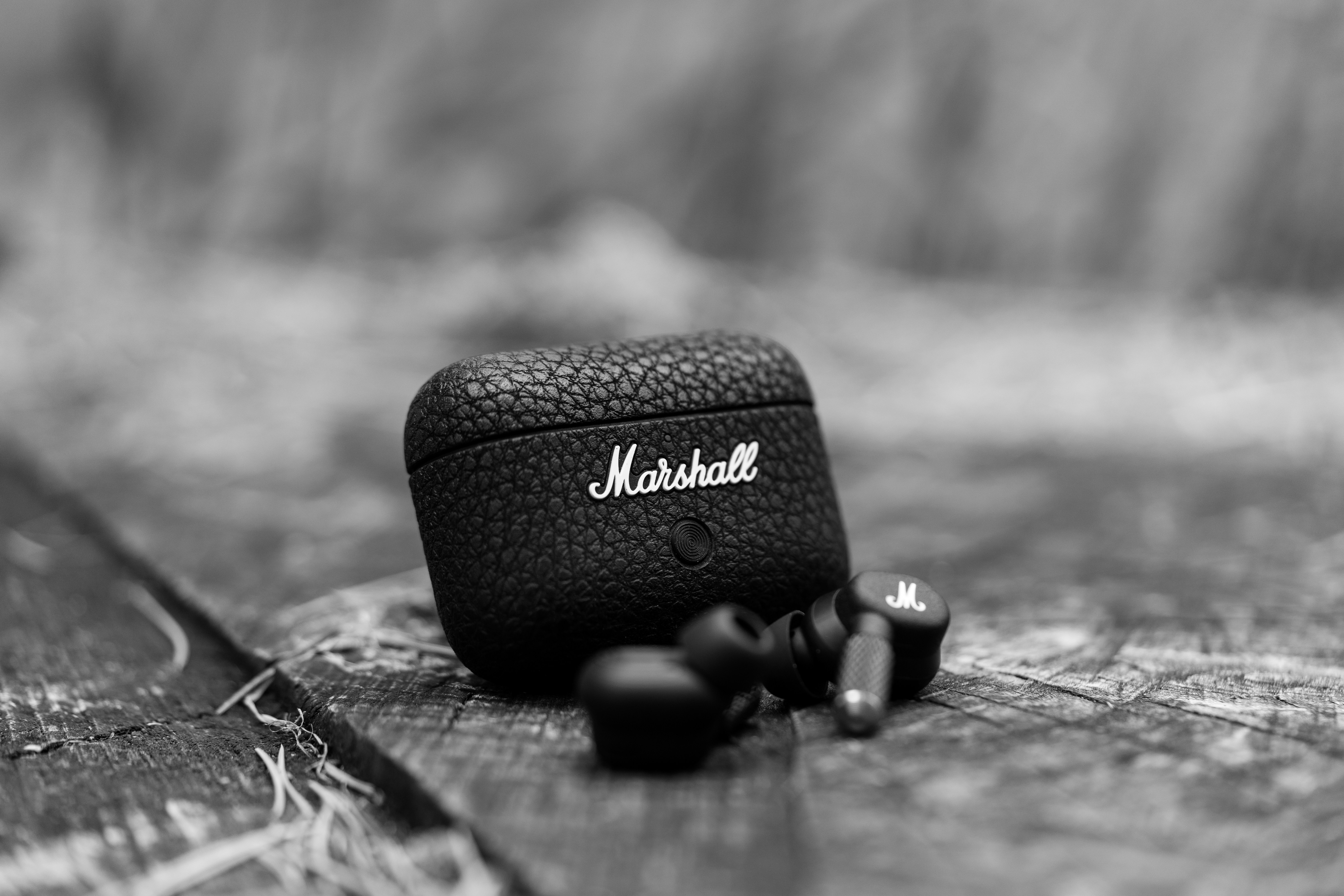 Black earbud case and earbuds on a weathered wooden surface.