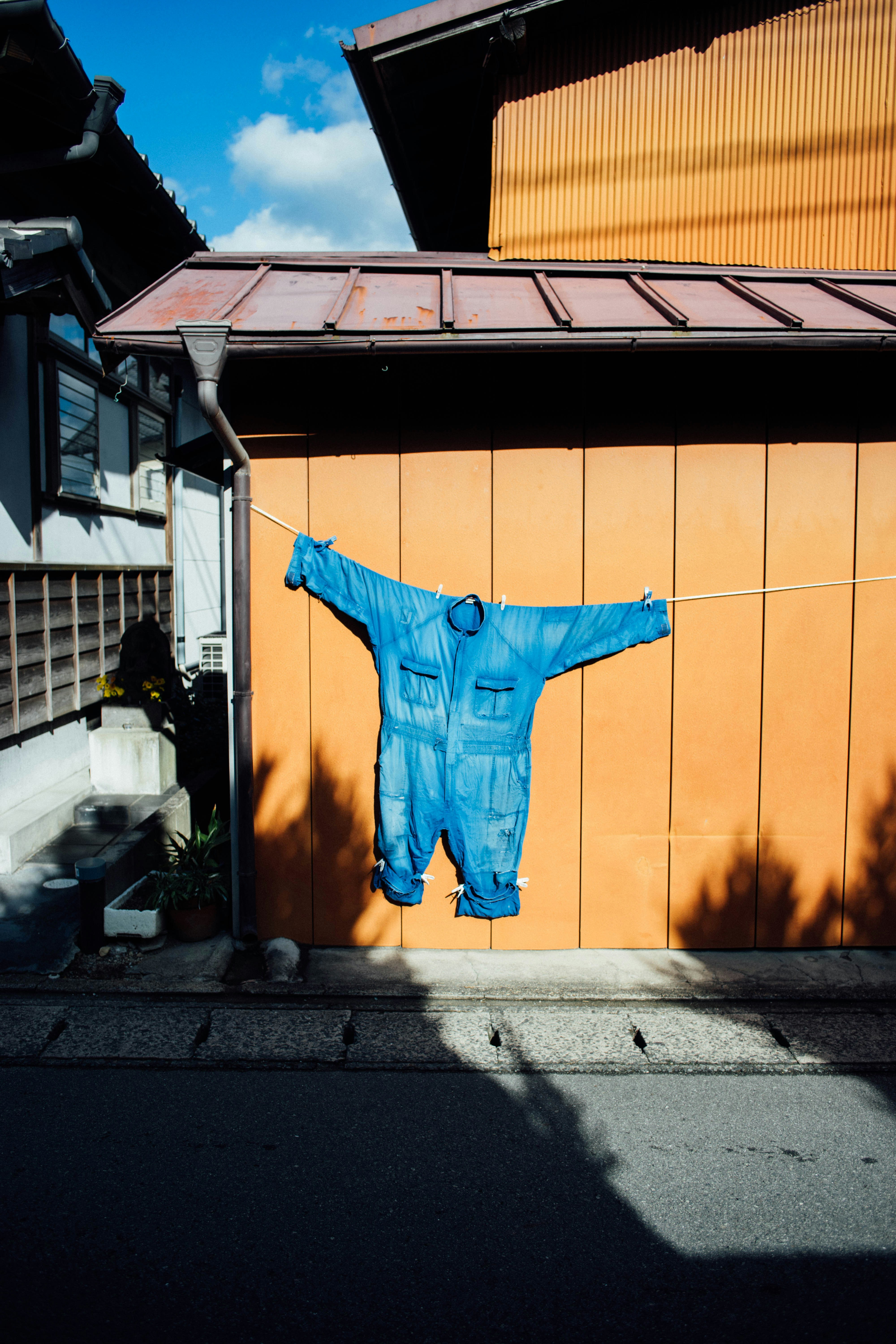 Azure Jumpsuit on a Sunlit Orange Wall: A Quiet Street Portrait
