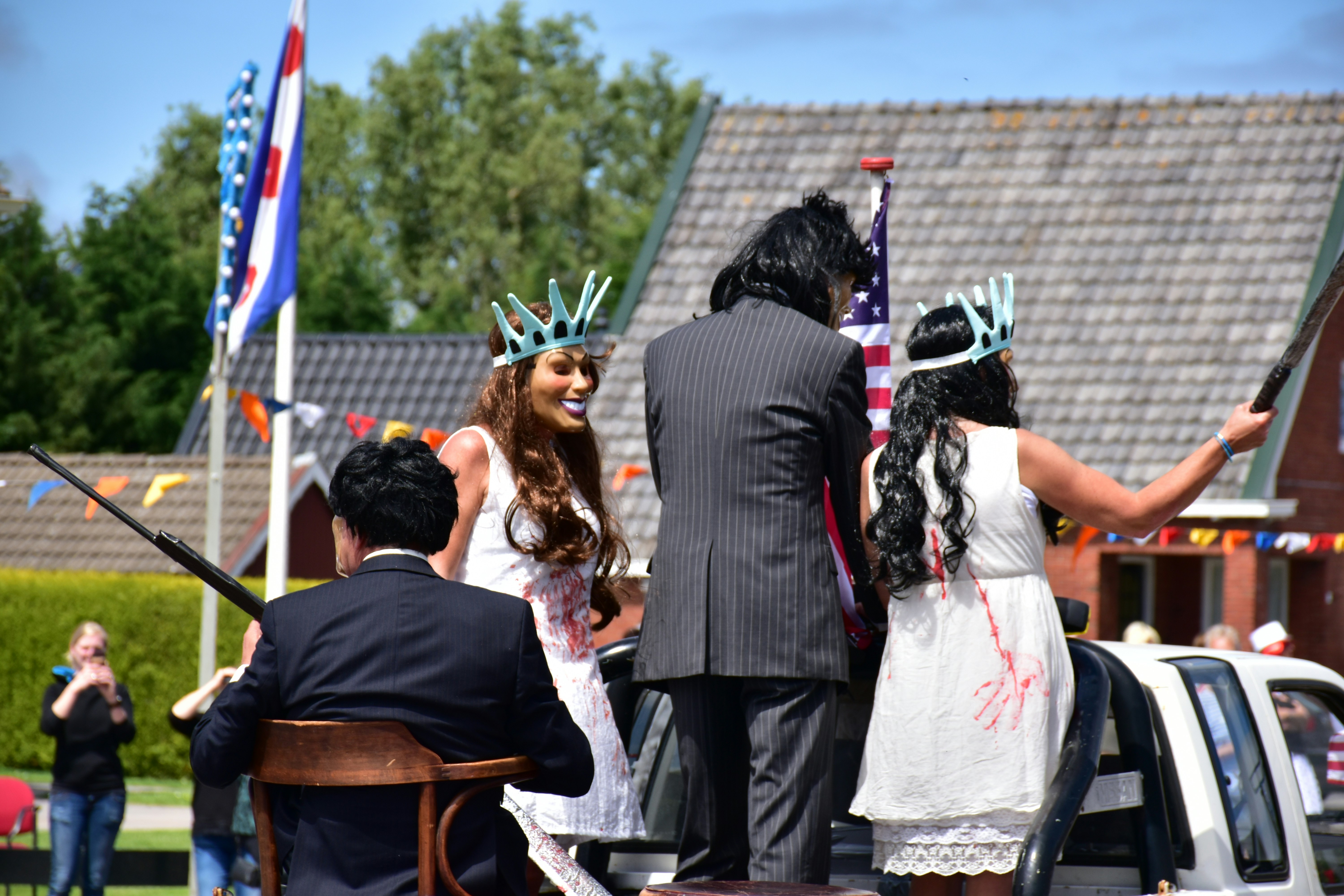 Participants in costumes reminiscent of the Statue of Liberty and a suited figure engage in a lively parade, showcasing a blend of celebration and satire.
