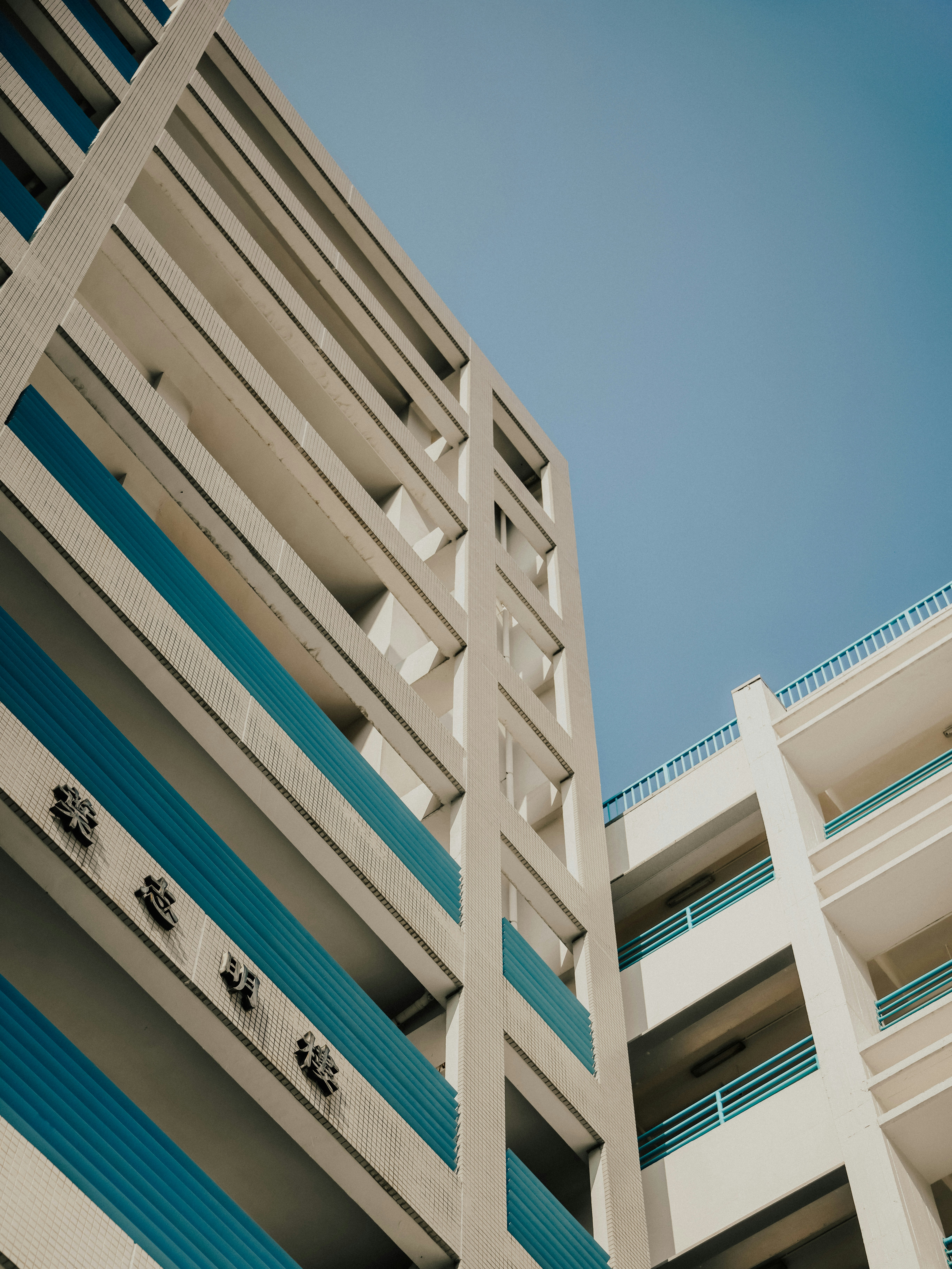 Modern architecture with beige and teal elements against a clear blue sky, highlighting vertical lines and symmetry.