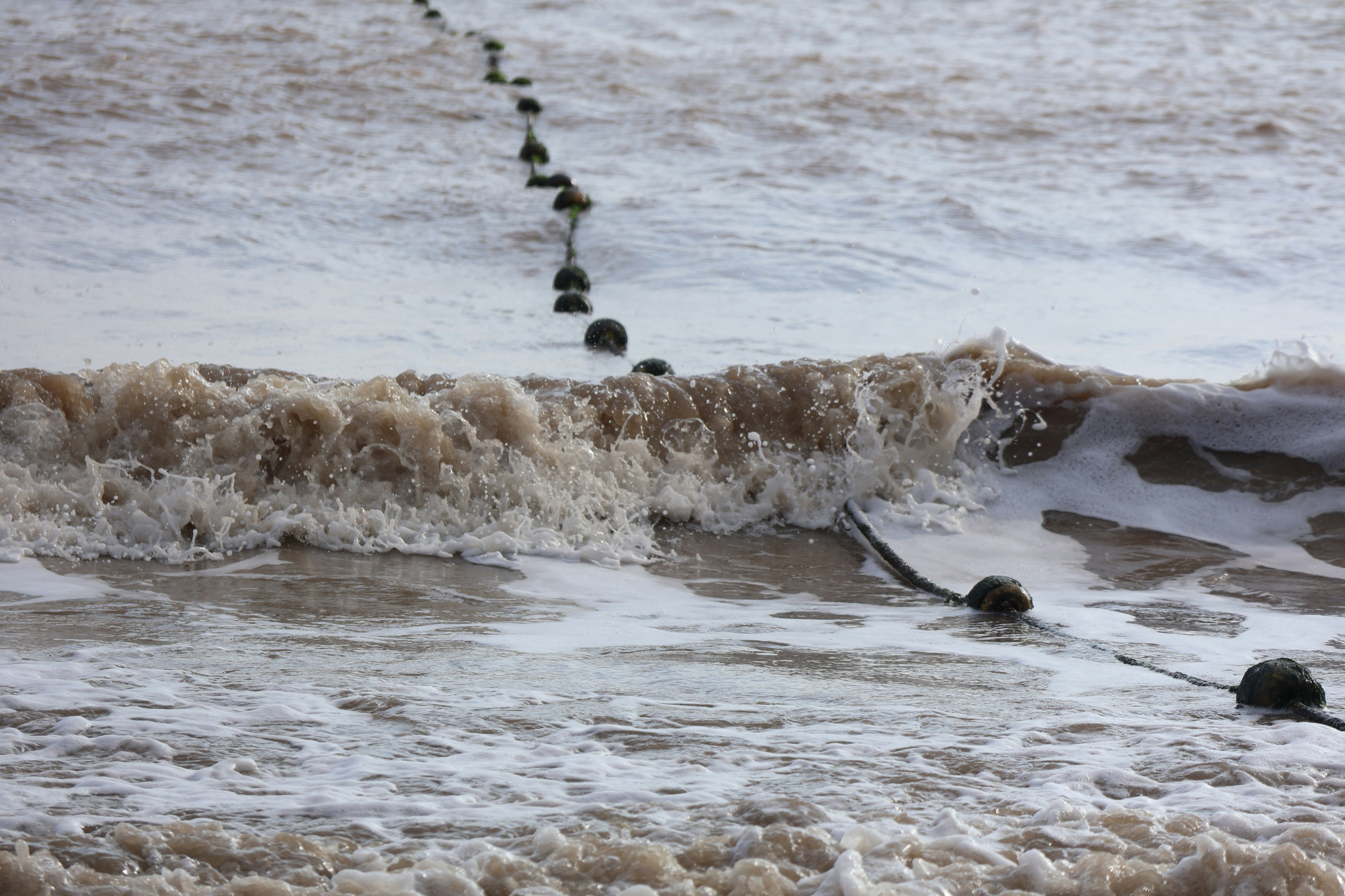 A long line of rocks sticking out of the water photo – Free Beach Image ...