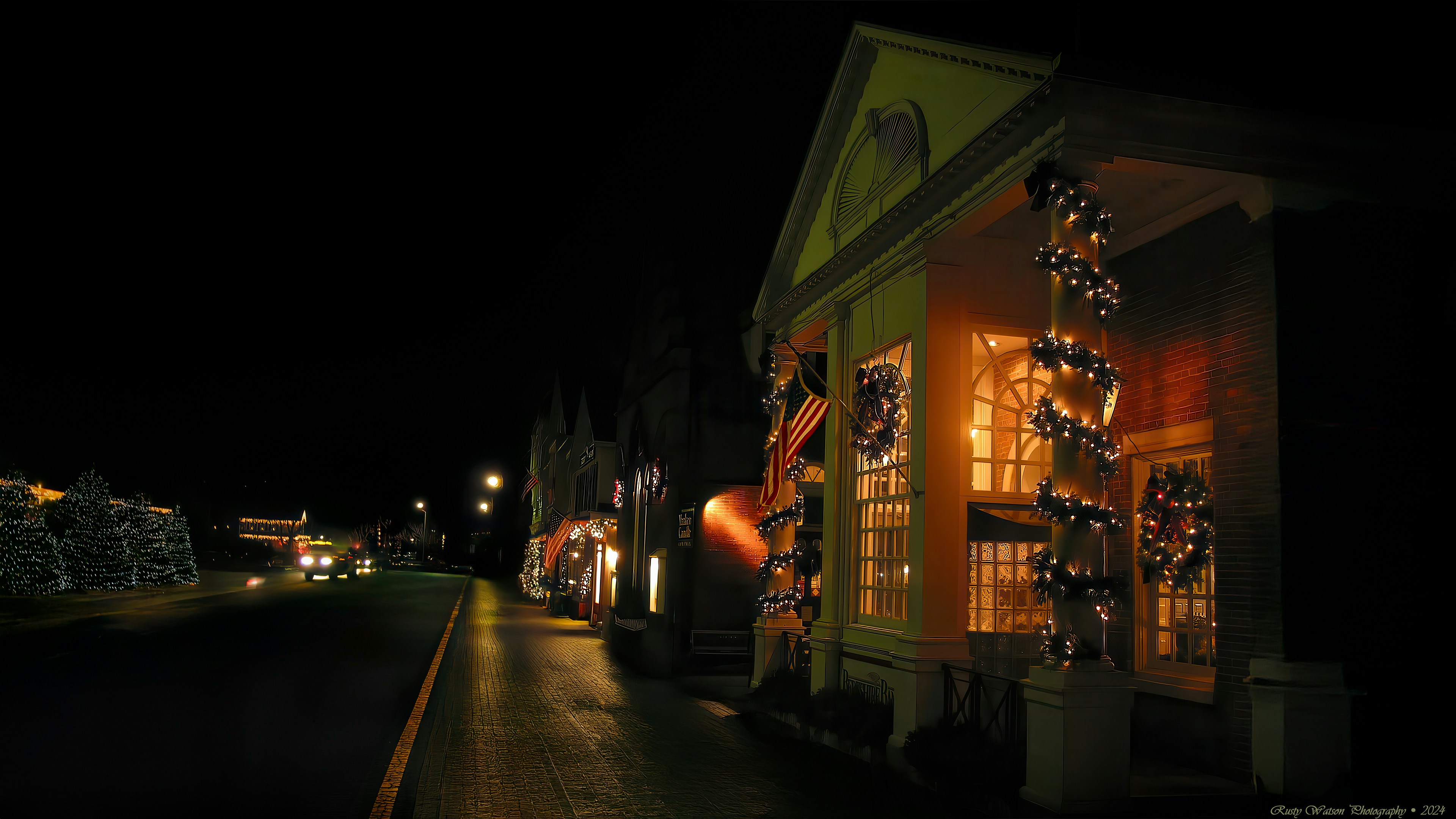 Street illuminated by holiday lights with decorated buildings at night.
