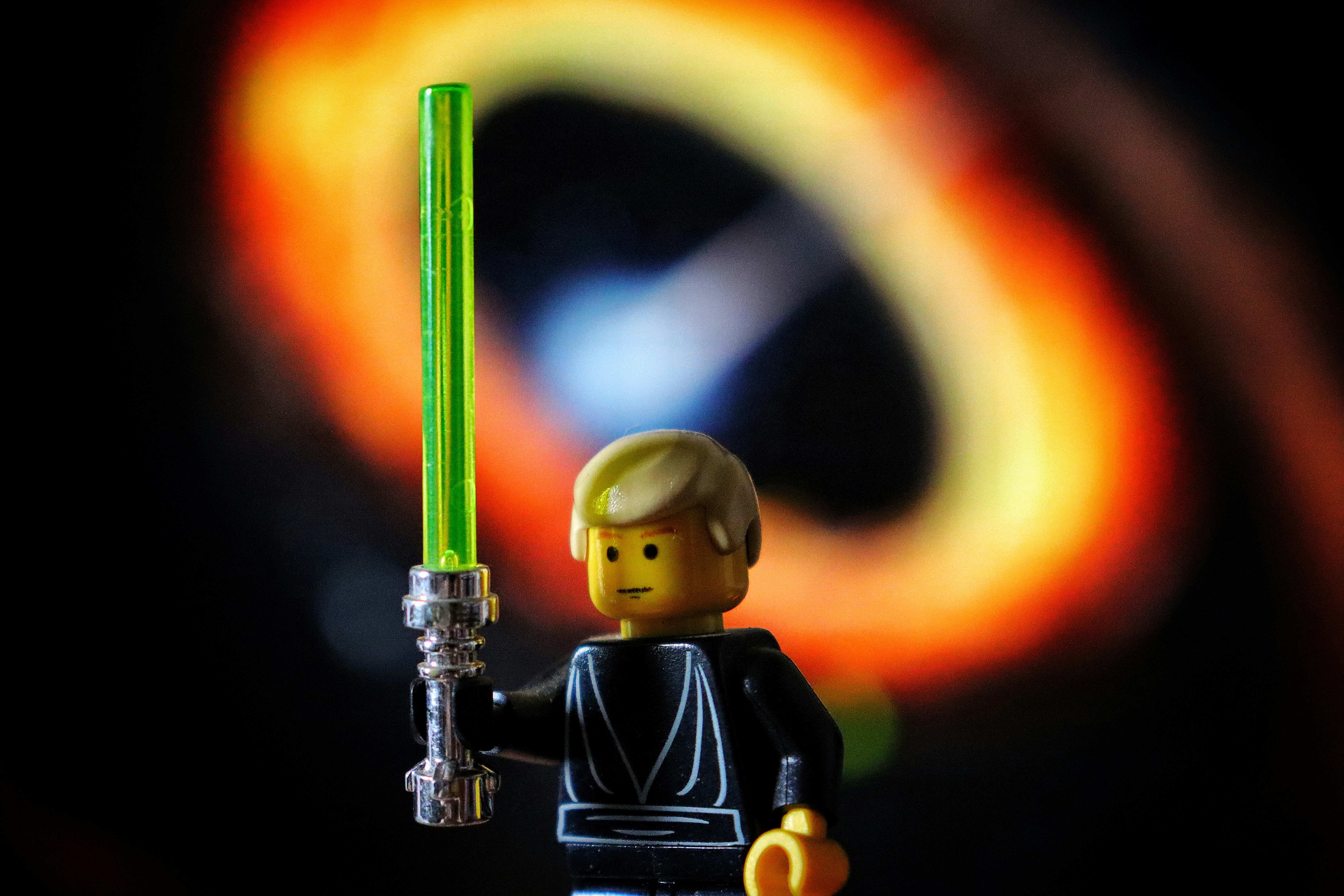 Close-up photograph of a LEGO minifigure wielding a green lightsaber. The scene features a luminous circular bokeh background that emphasizes the figure's silhouette.