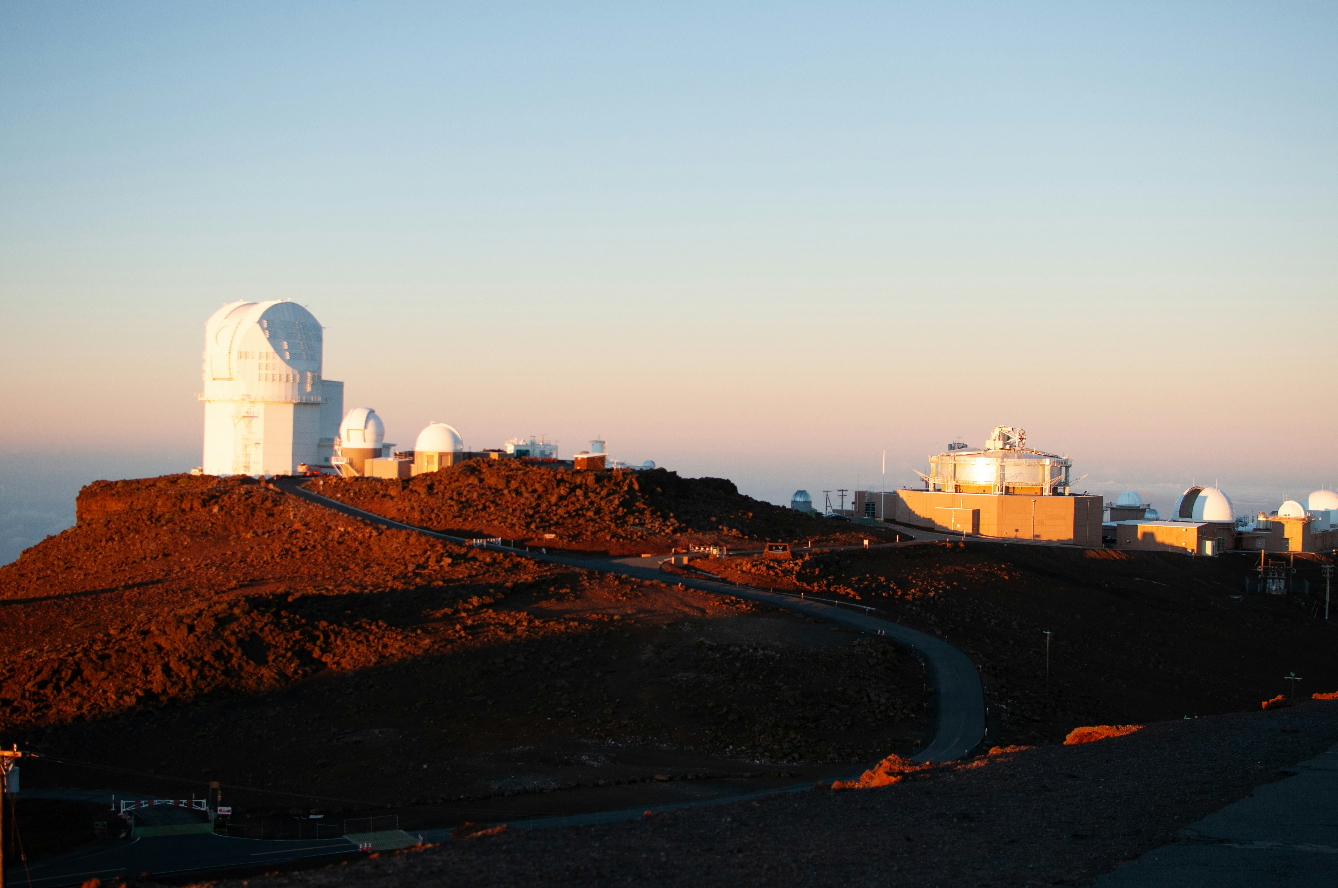 Haleakala Observatory at sunrise, casting warm light on rocky terrain and white domes.