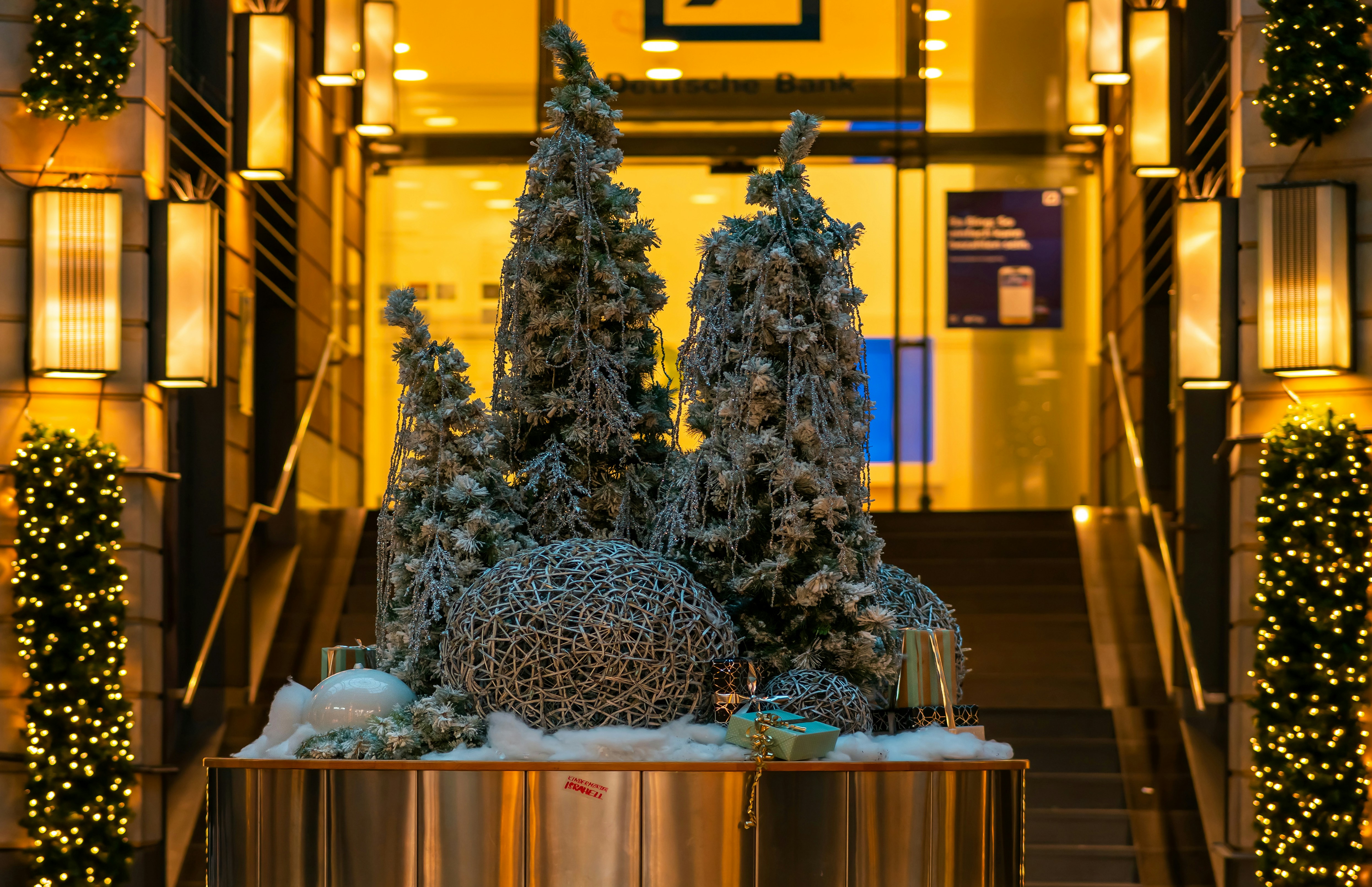 Snow-Dusted Conifers and Metallic Orbs Under Golden Mall Lights