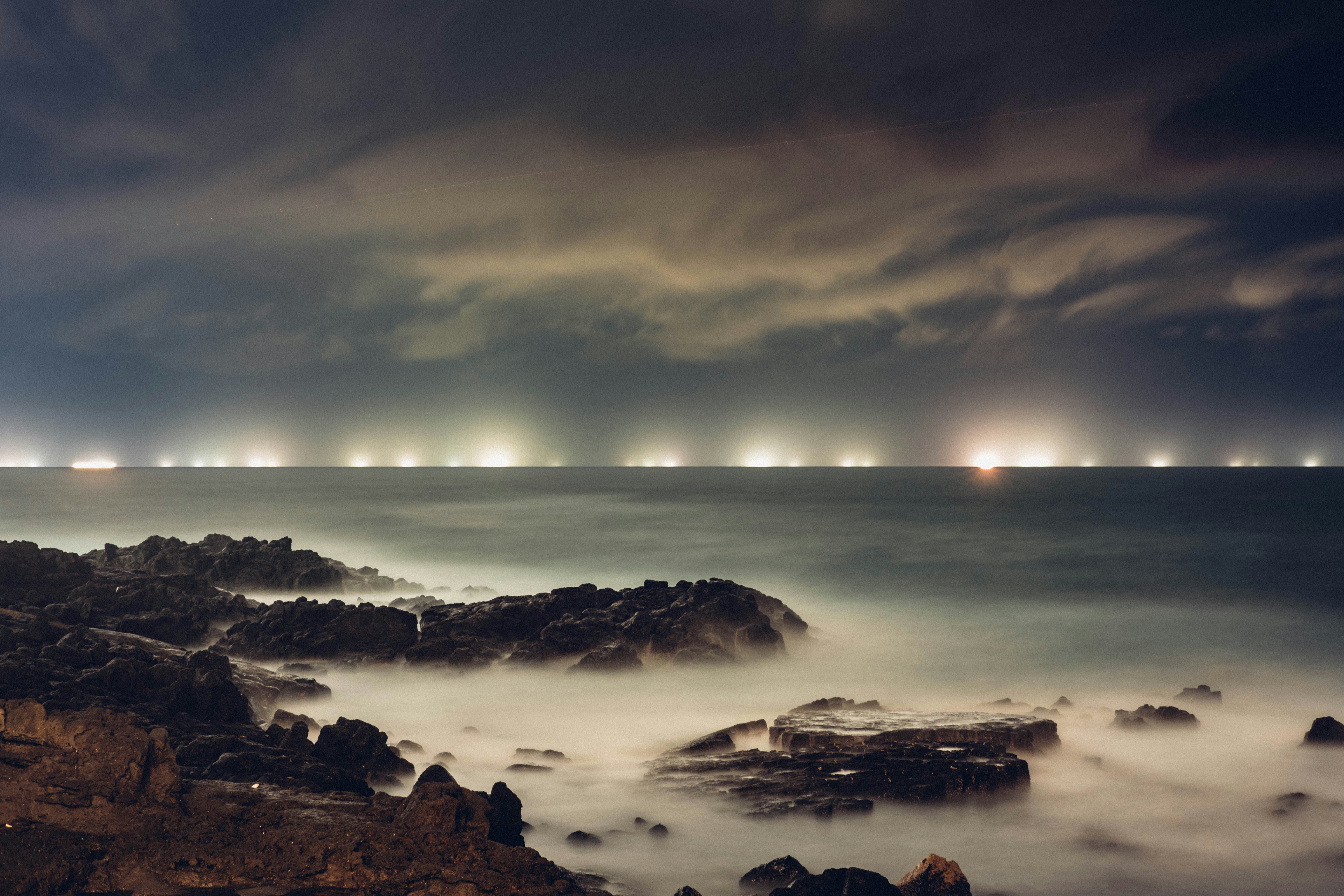 Rugged Shoreline at Night: Harbor Lights Trace a Velvet Sea