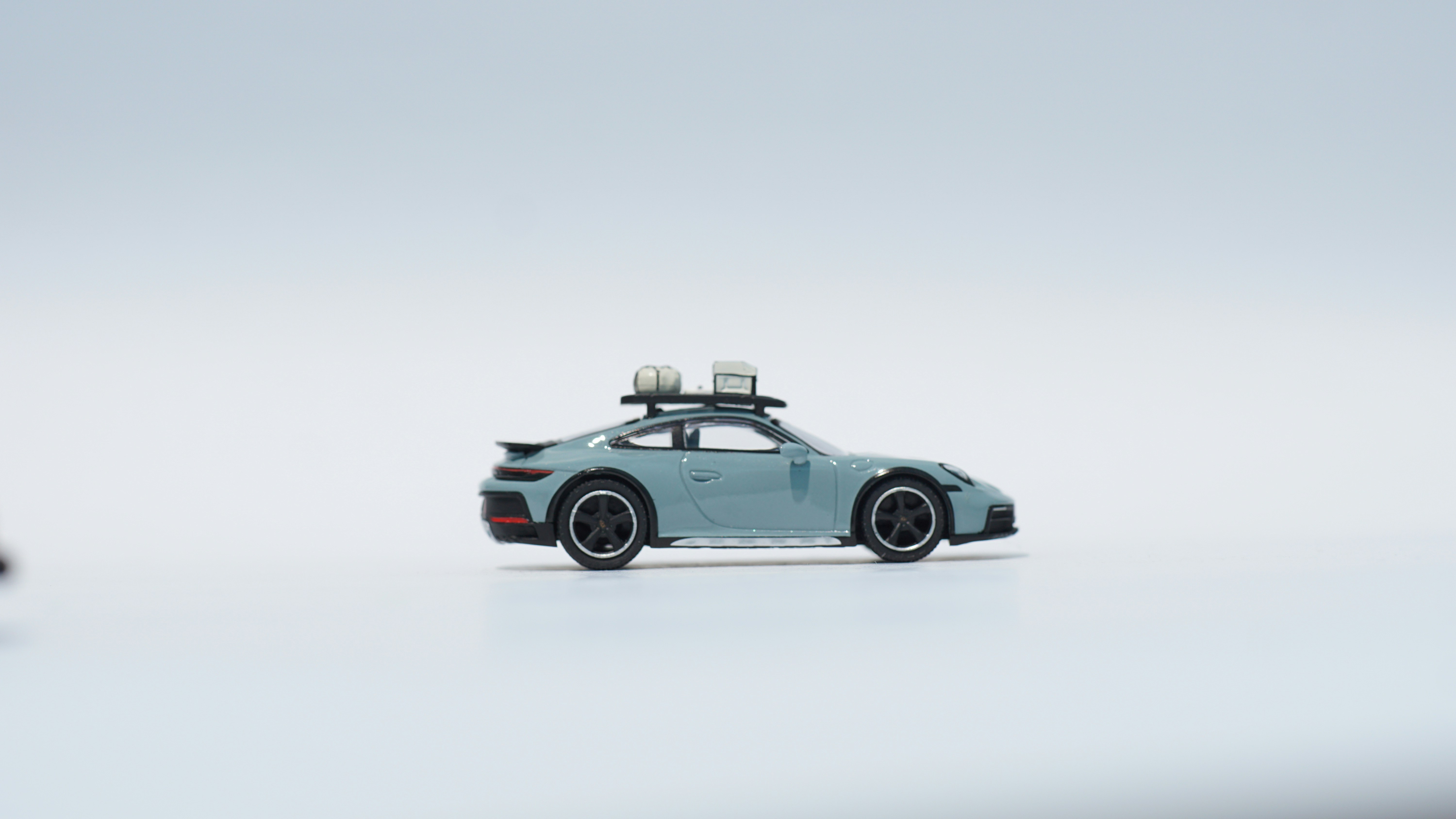 Detailed model of a Porsche with rooftop cargo against a minimalist backdrop.