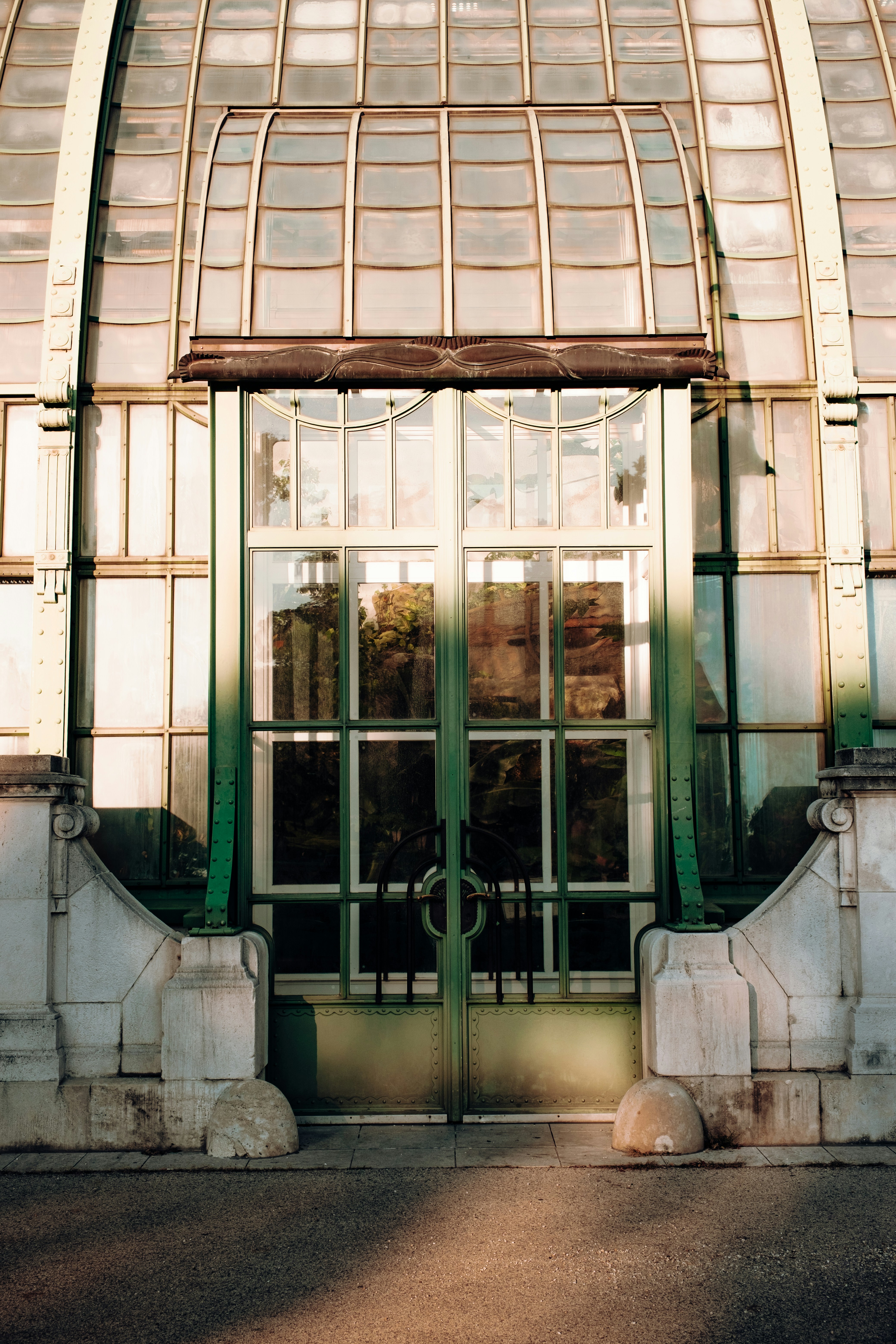 Sunlit green metal-framed glass doors of a conservatory, casting soft shadows on the pavement.