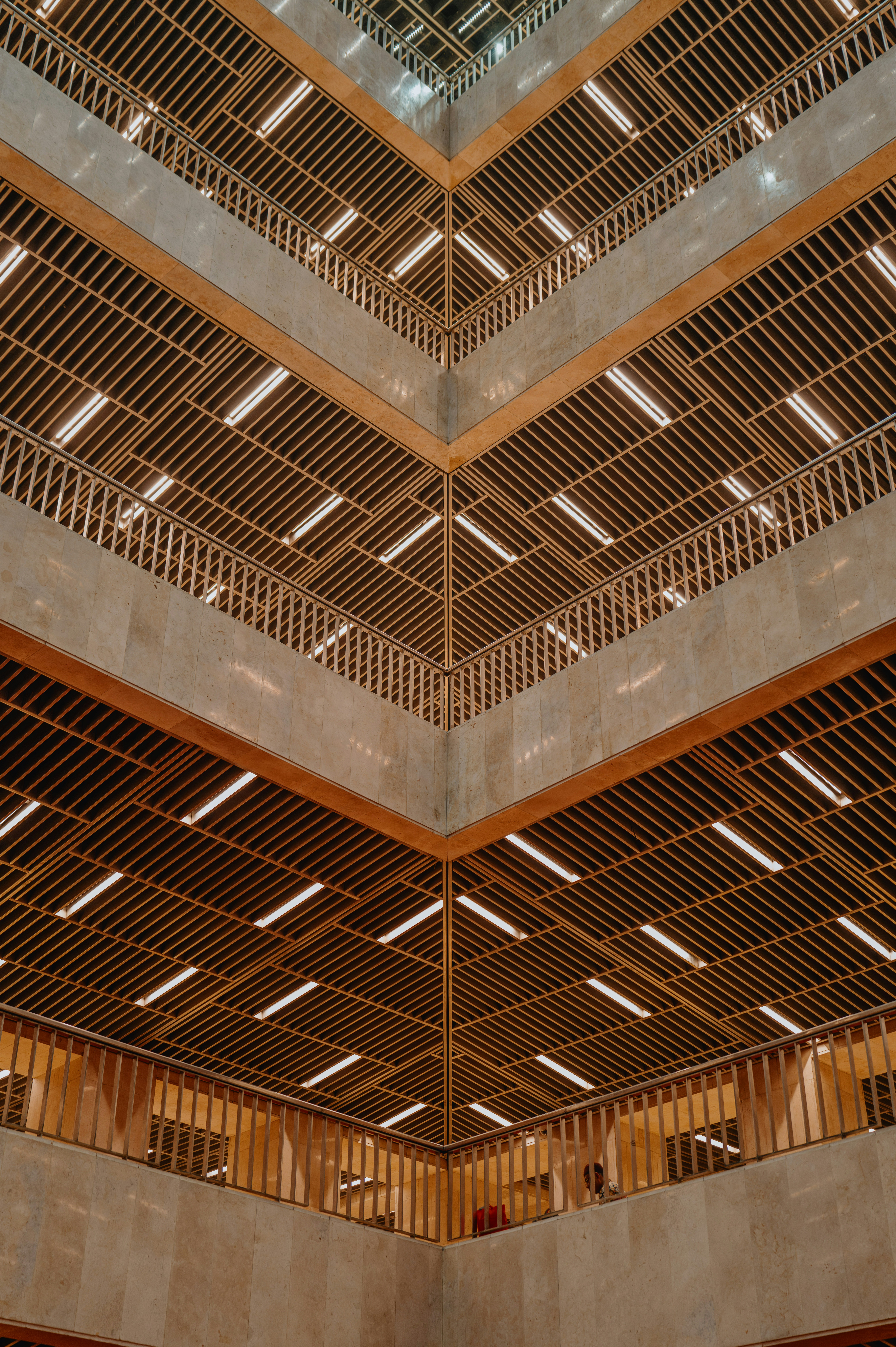 Geometric atrium with staggered concrete balconies and warm lighting. Converging chevrons draw the eye toward the central intersection.