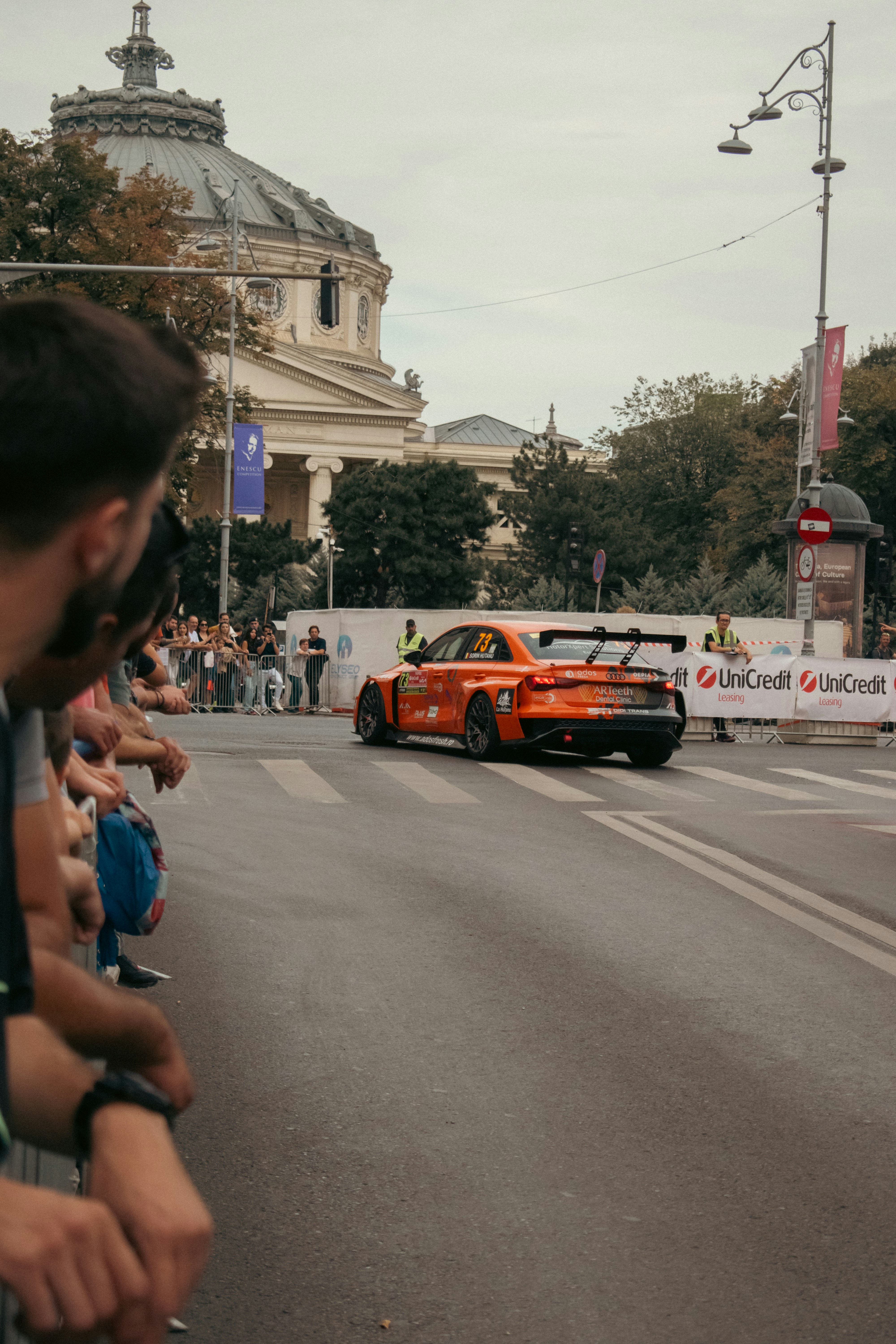 Urban Sprint by the Dome: An Orange Race Car Slices Through Barricades