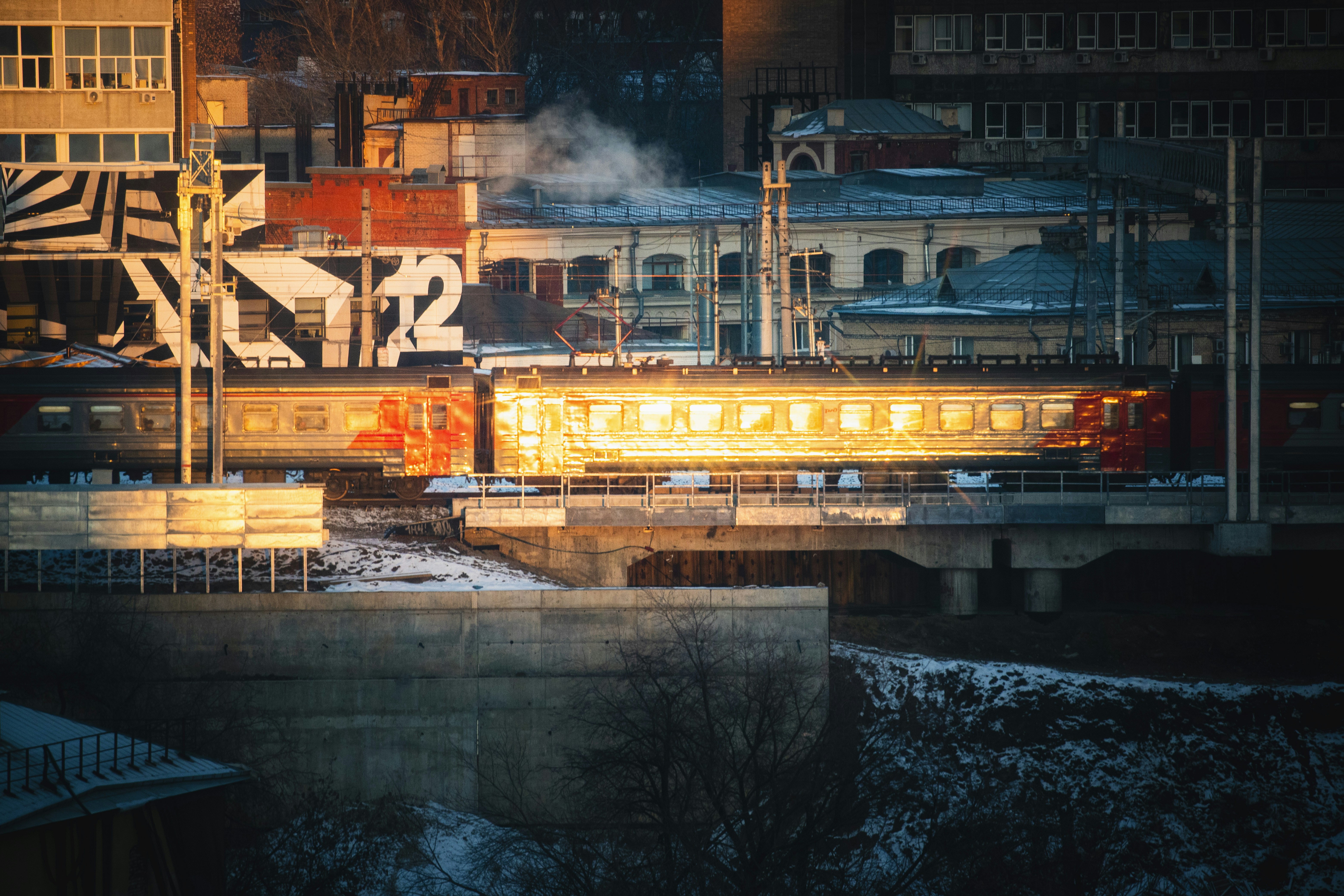 Glowing Orange Railcar Crossing a Snow-Dusted City Bridge