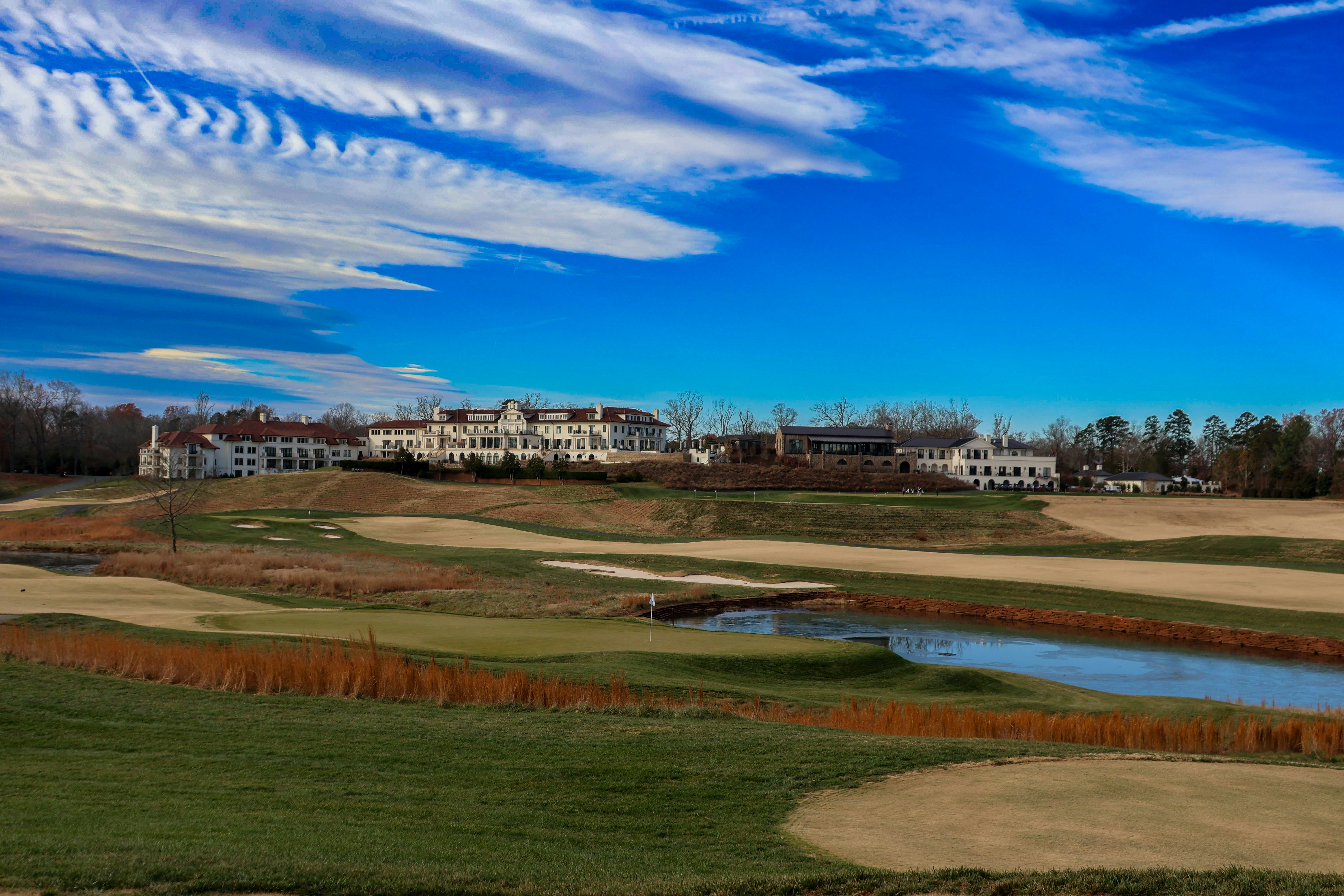 Row of white clubhouses rising above emerald greens under a cobalt sky
