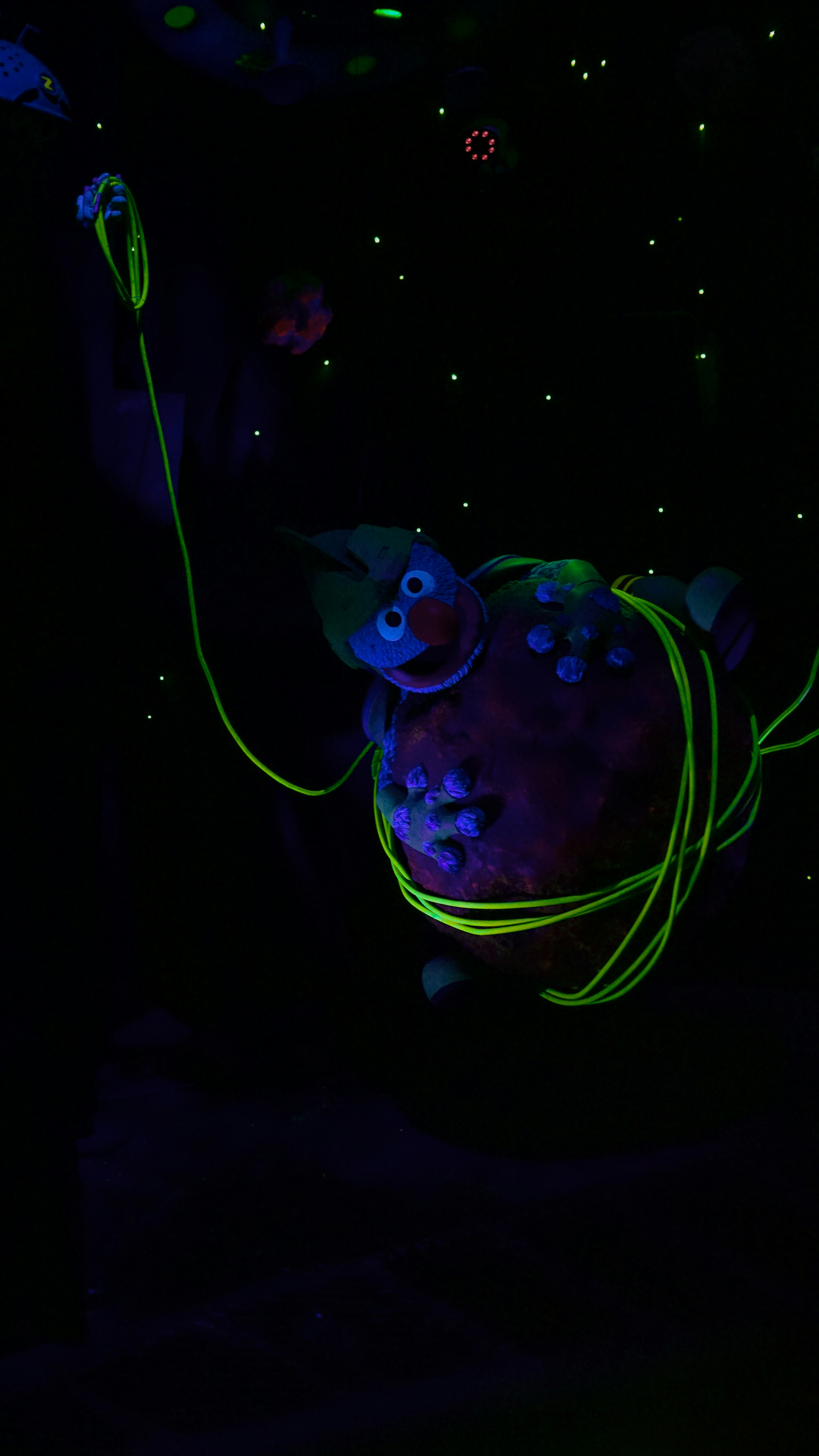 A colorful character entangled in glowing green cords, set against a dark backdrop speckled with faint lights.