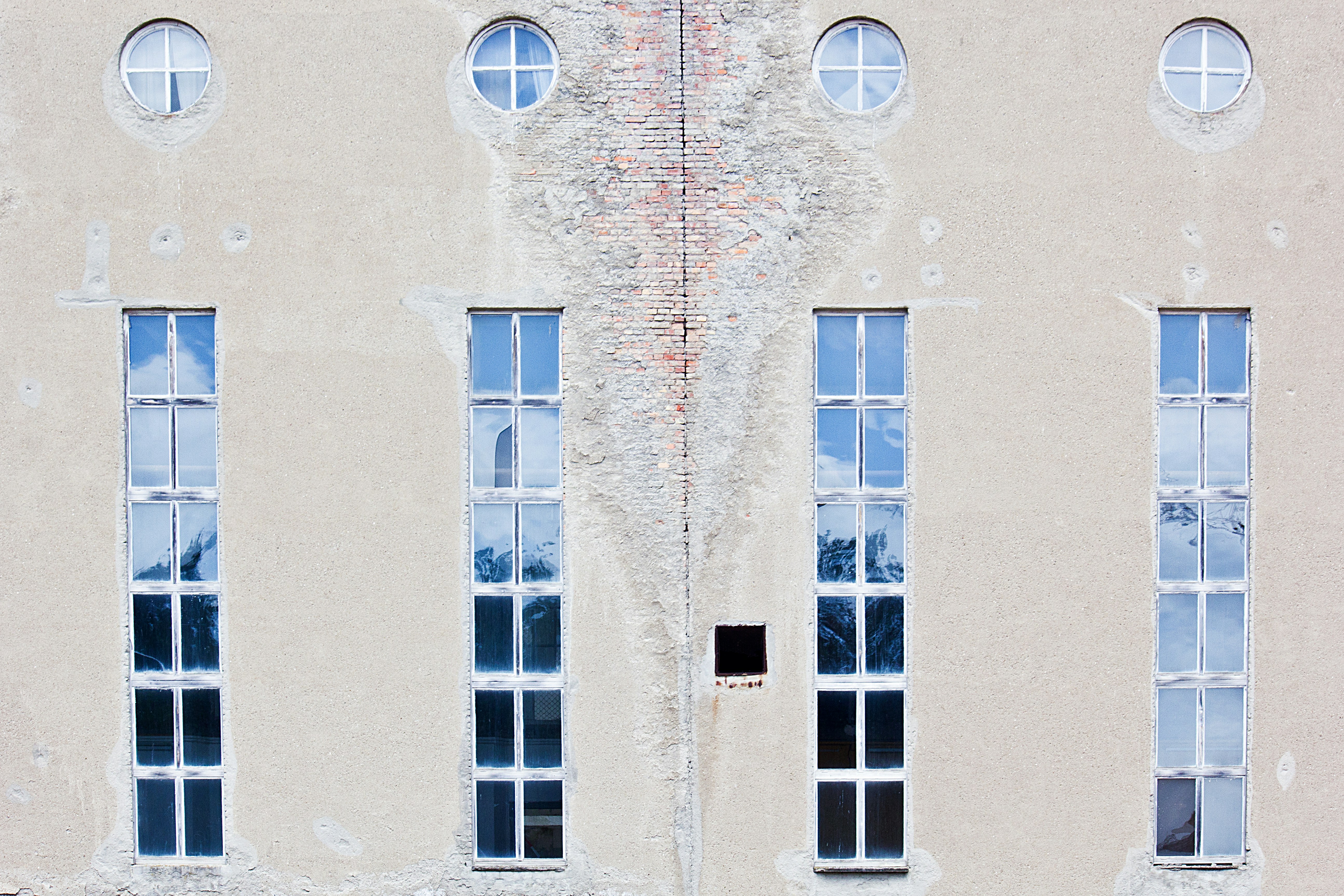 Tall windows reflecting a blue sky on a worn beige building facade.