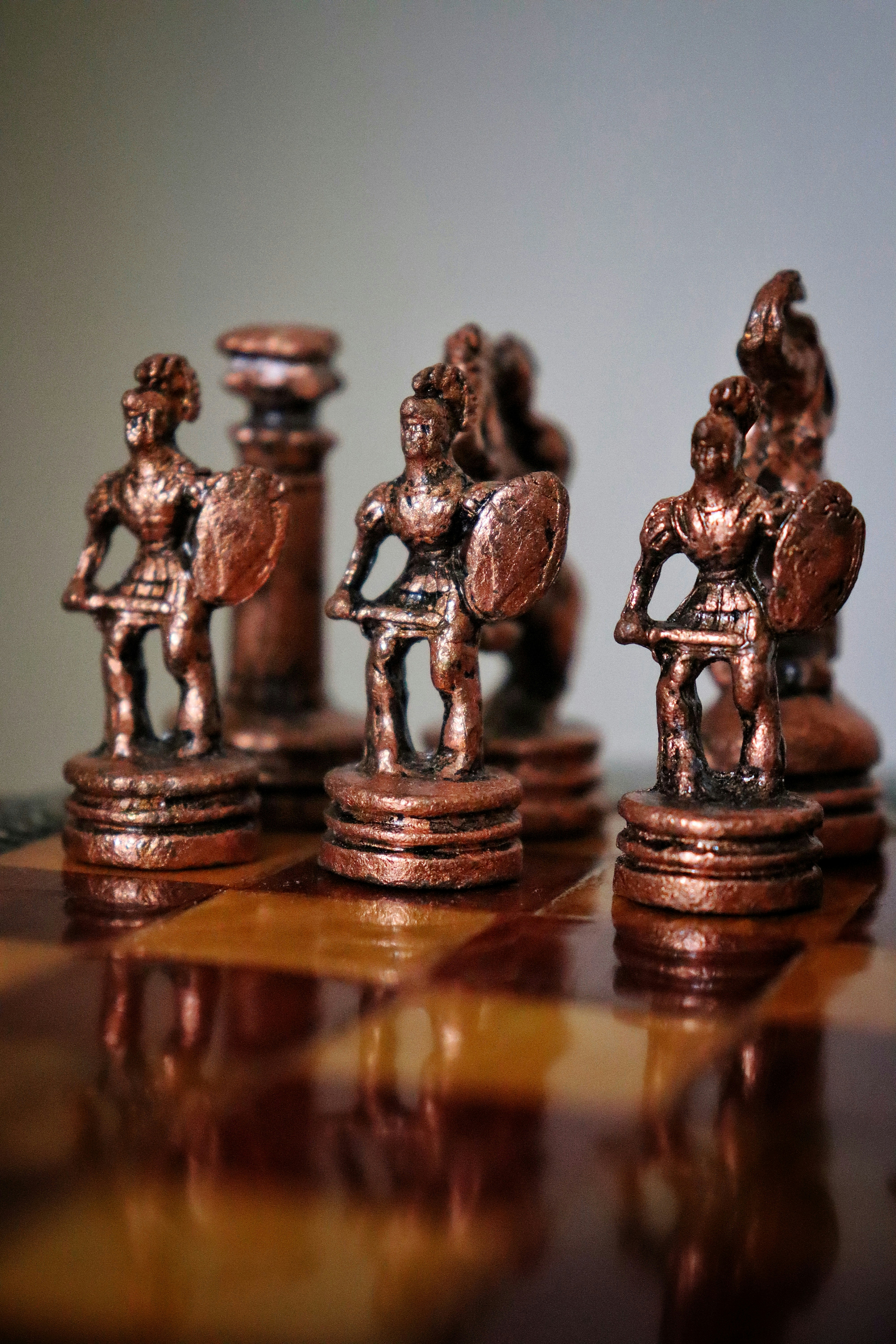 Bronze chess pieces resembling warriors on a wooden chessboard.