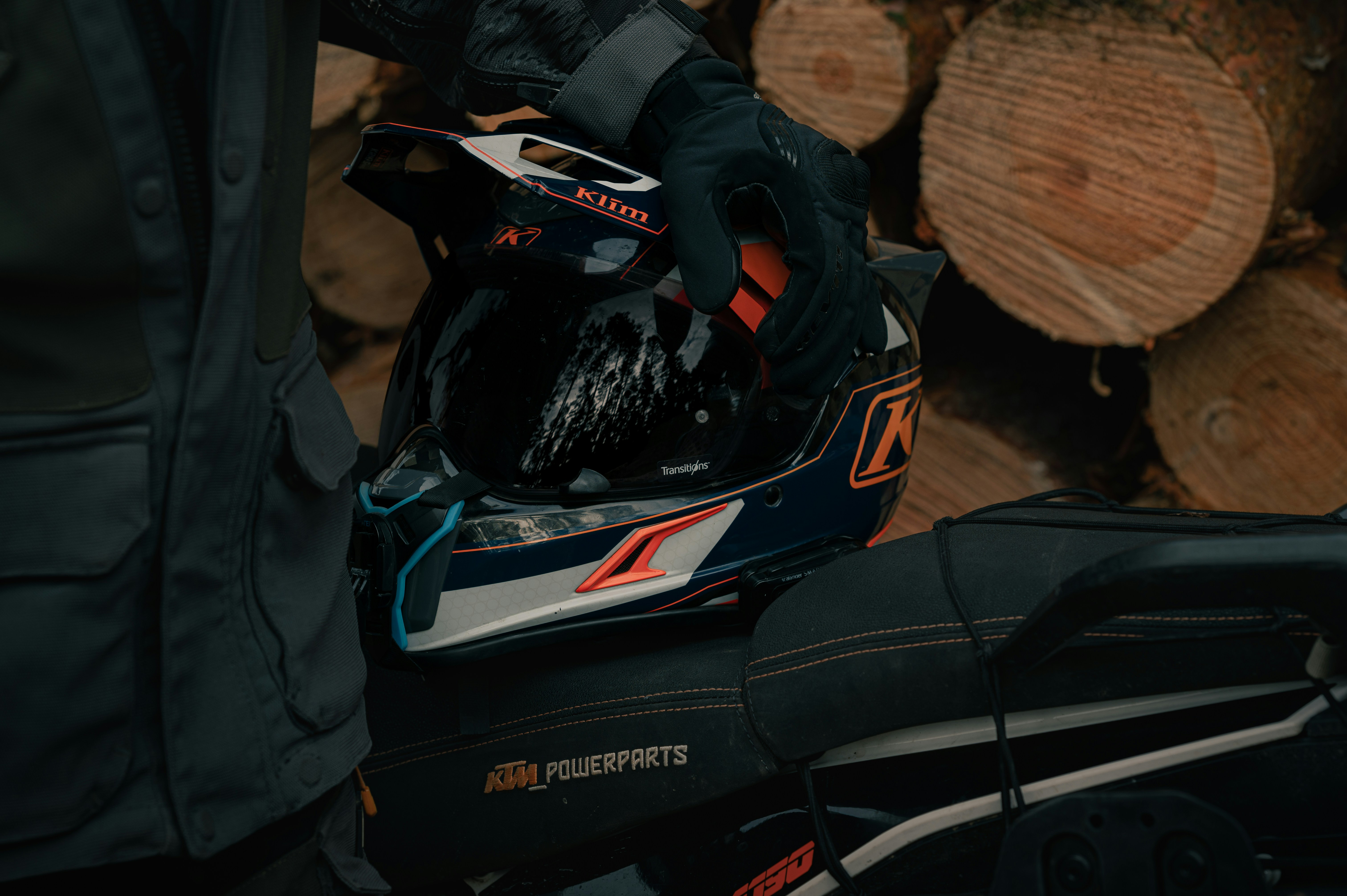 Dim workshop moment: a KTM helmet rests on a PowerParts box beside stacked logs.