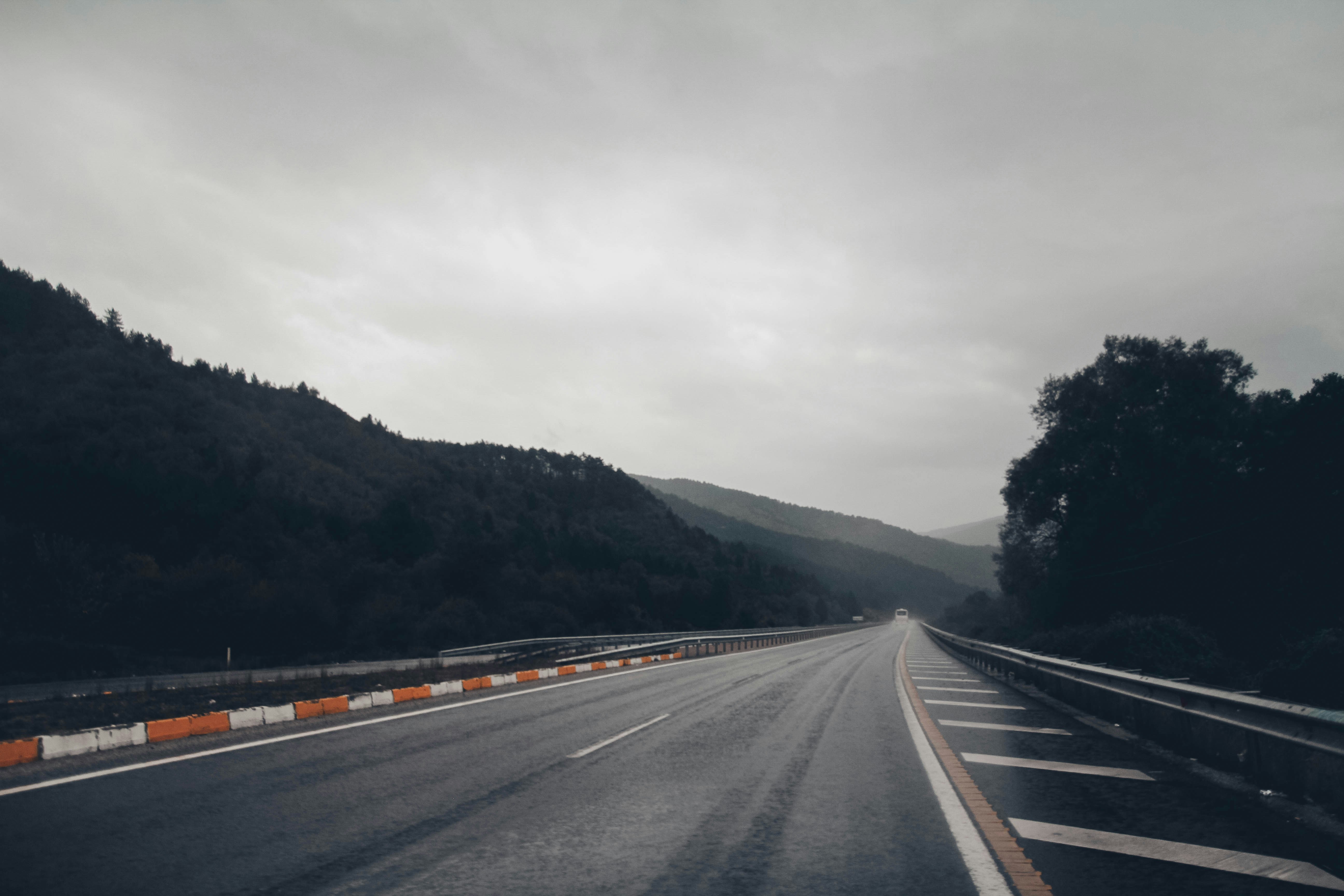 Empty highway stretching through misty forested hills under a cloudy sky.