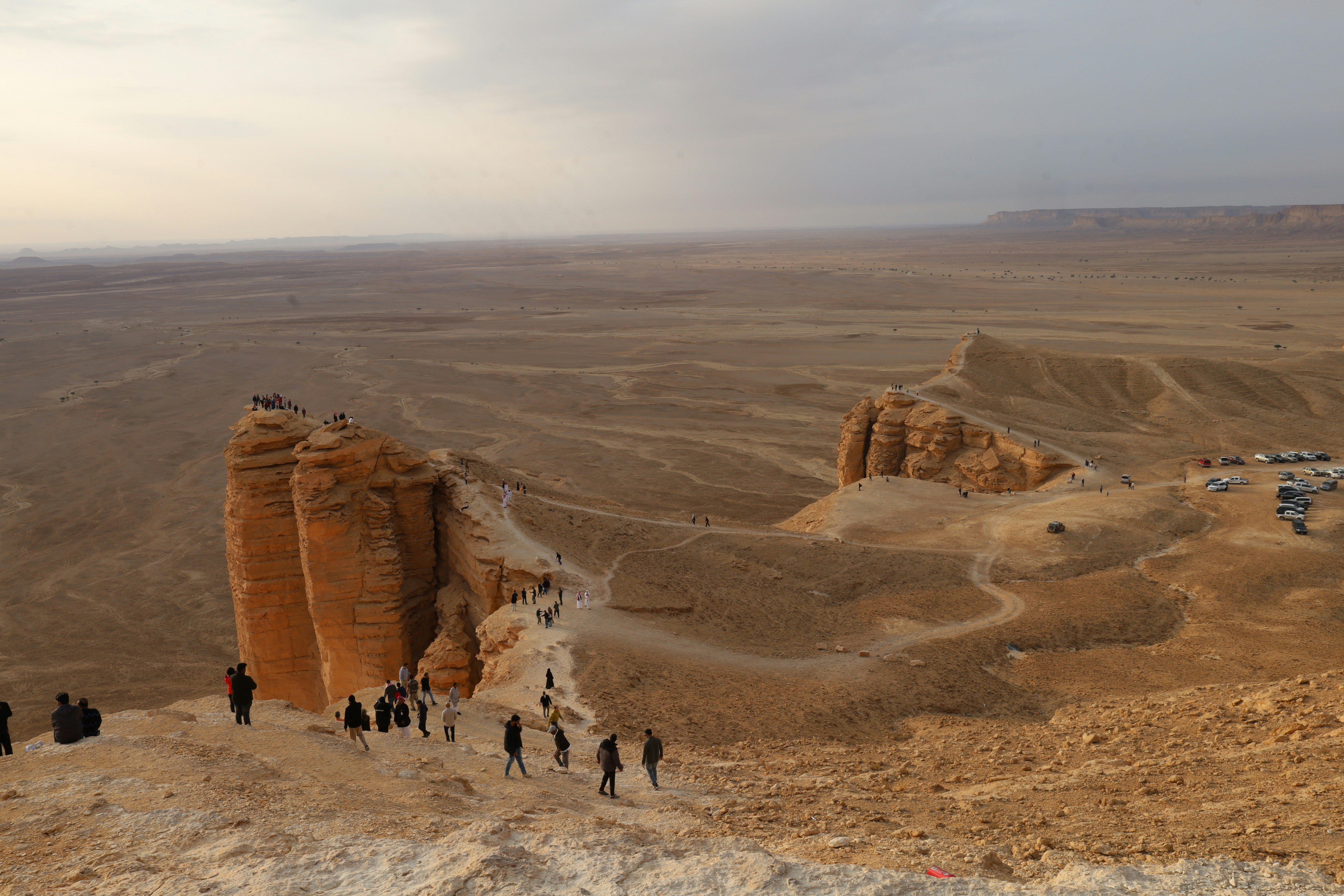 Hikers traverse winding paths around towering rock formations in a vast desert landscape.