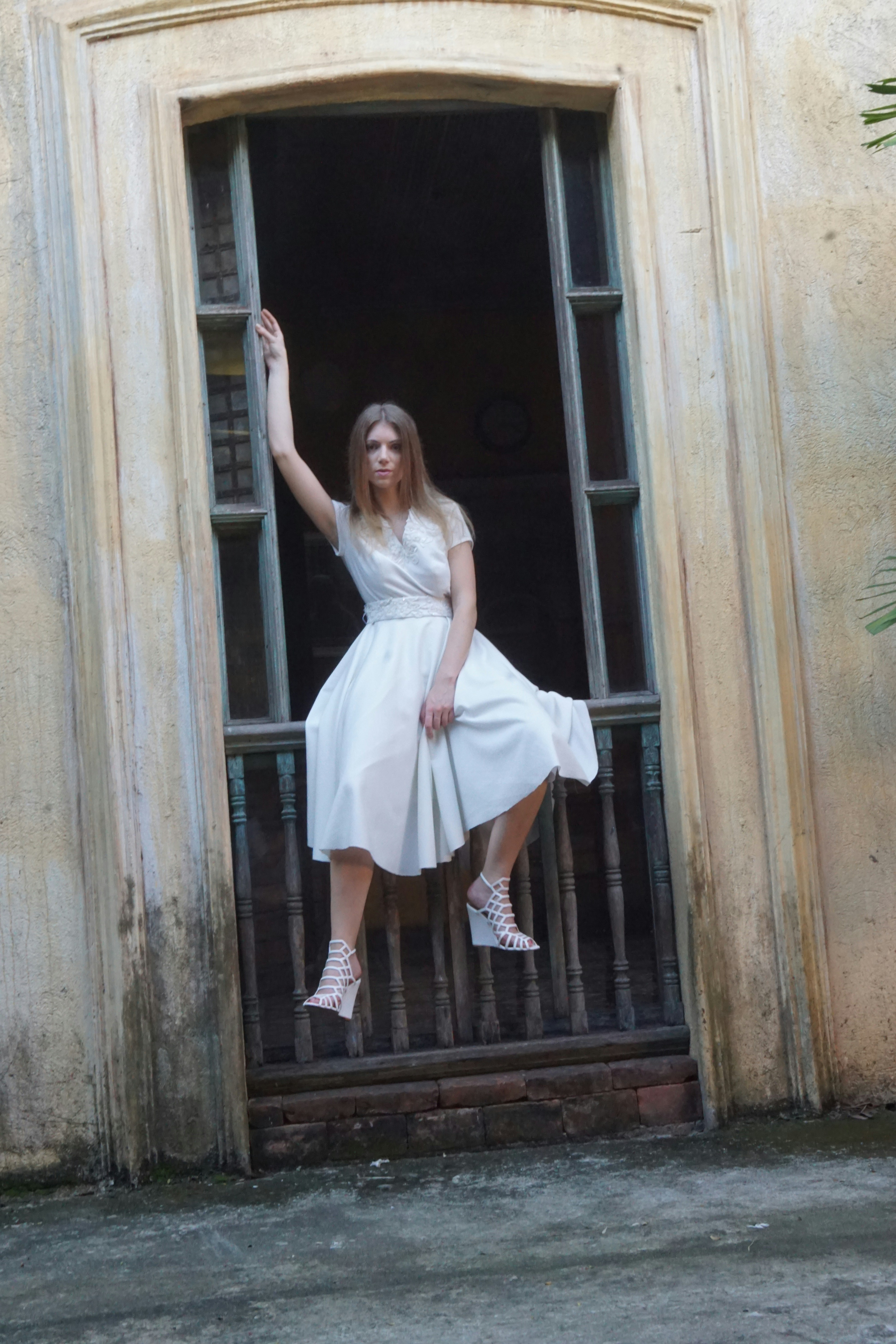 A woman in a white dress sitting on a window sill photo – Free Woman ...