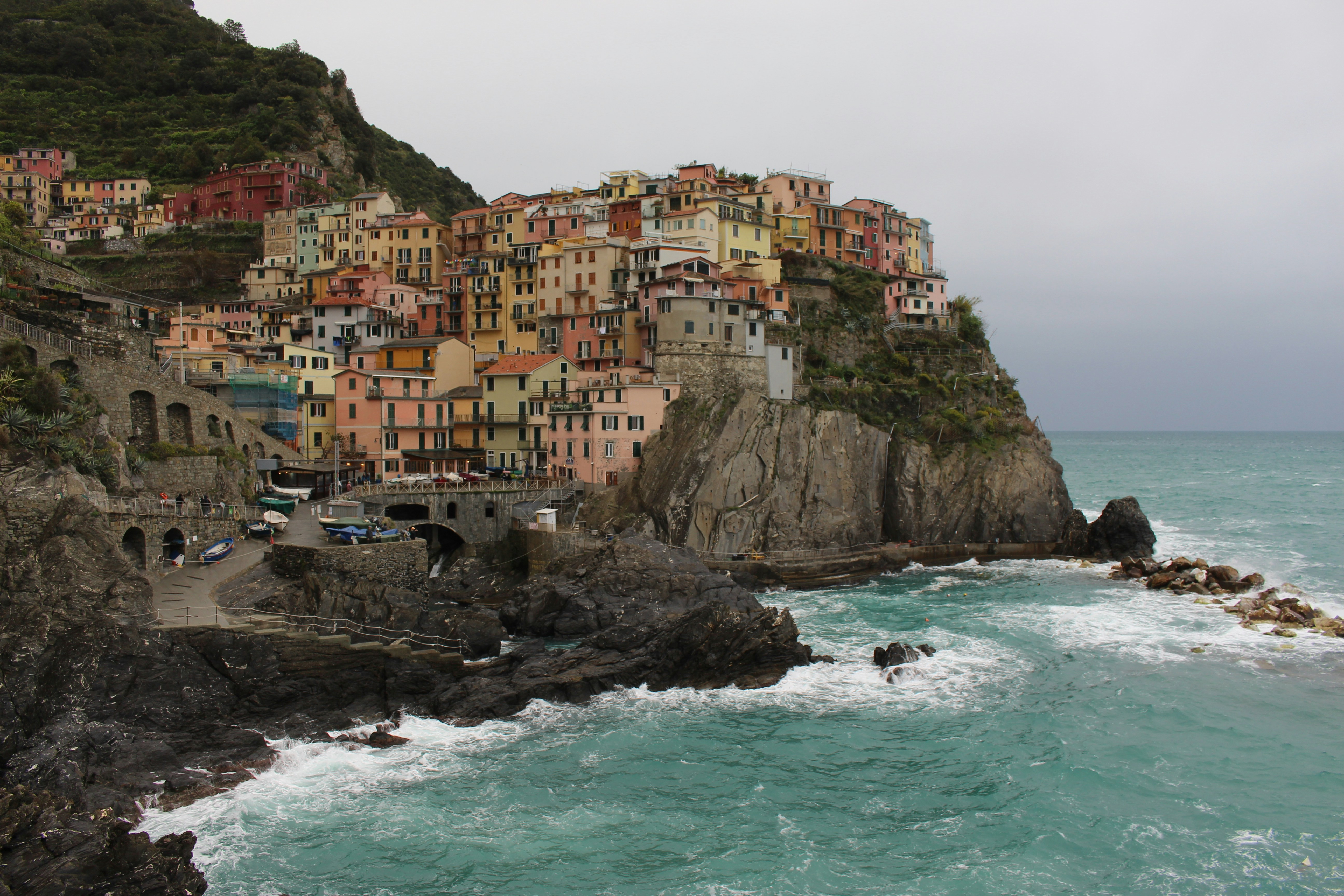 Vibrant cliffside village overlooking the turquoise sea, with colorful buildings cascading down the rocky shoreline. Waves crash against the coast.
