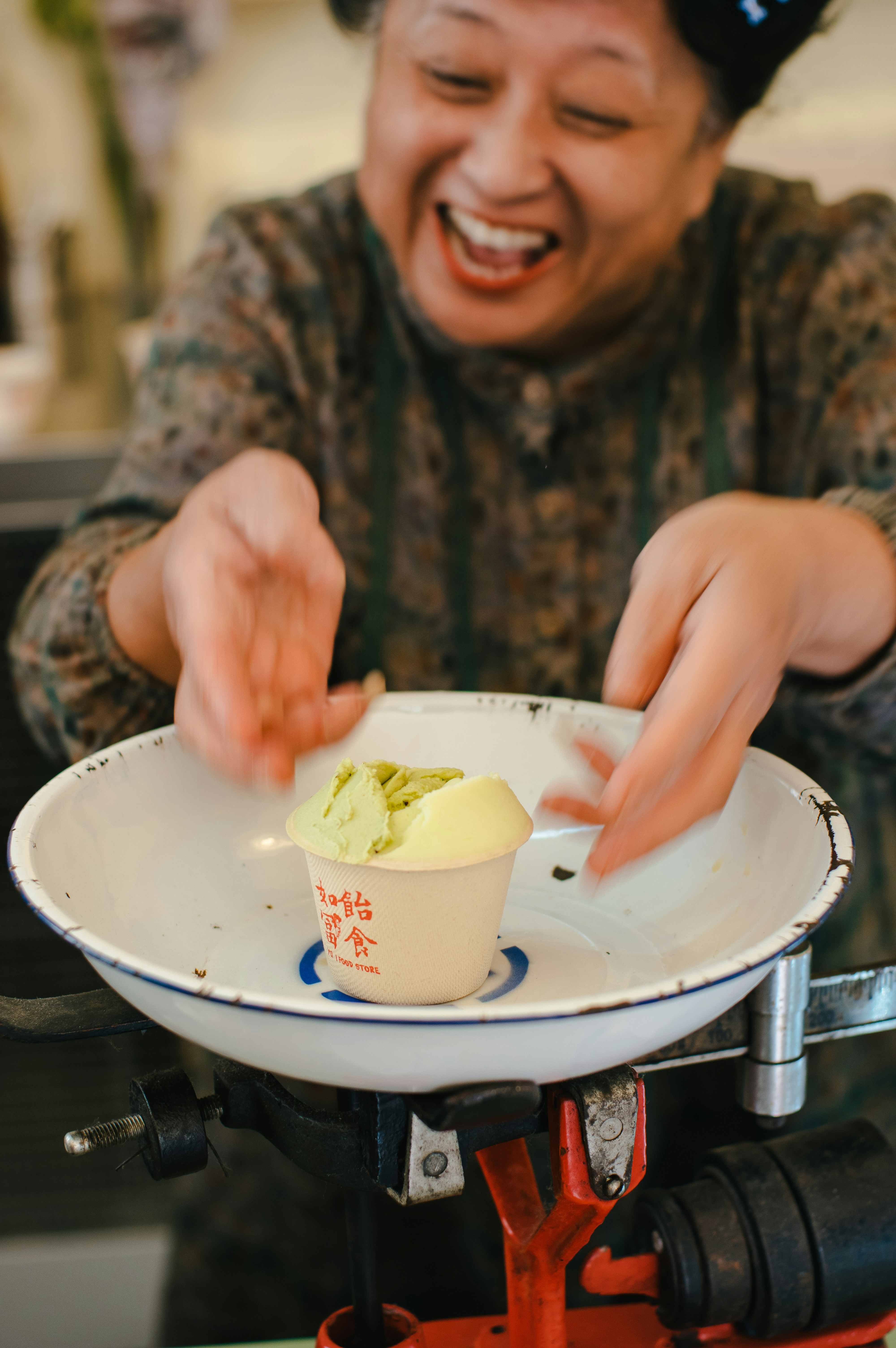 Small ice cream cup sits on a vintage balance scale as a vendor scoops, capturing a candid, joyful moment.