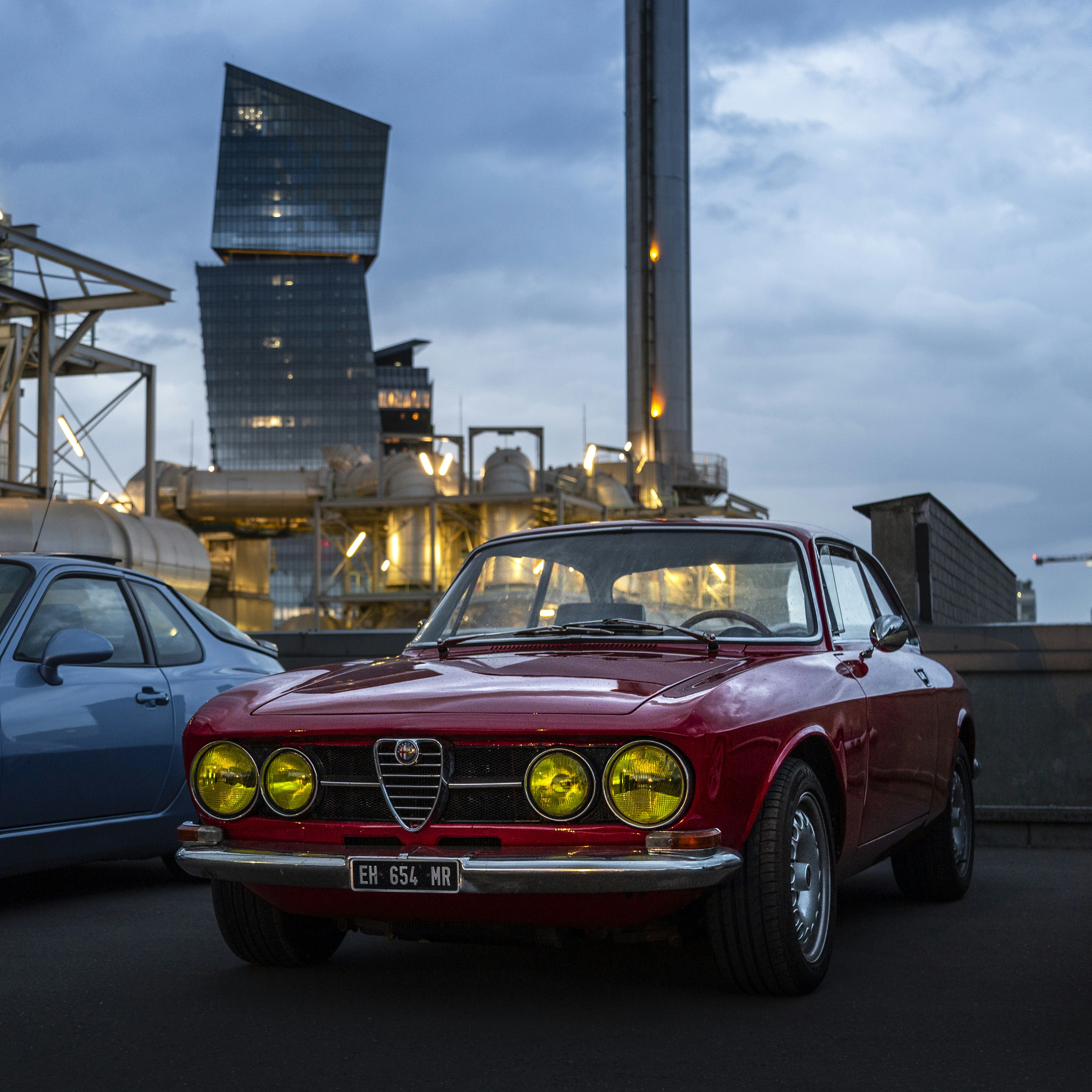 Rooftop Rendezvous: A Crimson Classic Poses Against a Steel Skyline at Blue Hour