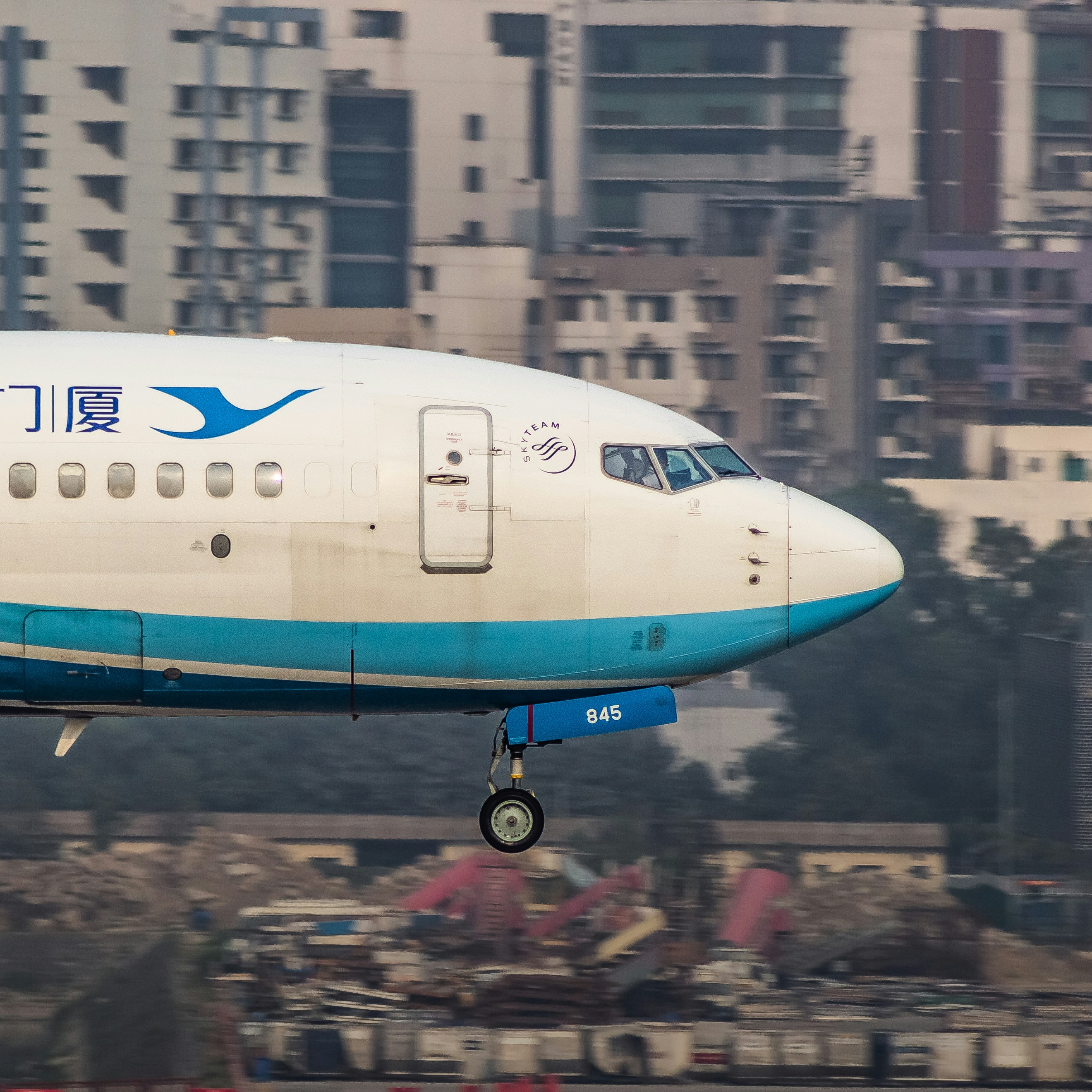 Nose in Focus, Cityscape in the Backdrop: A Turquoise-Bellied Airliner on Approach
