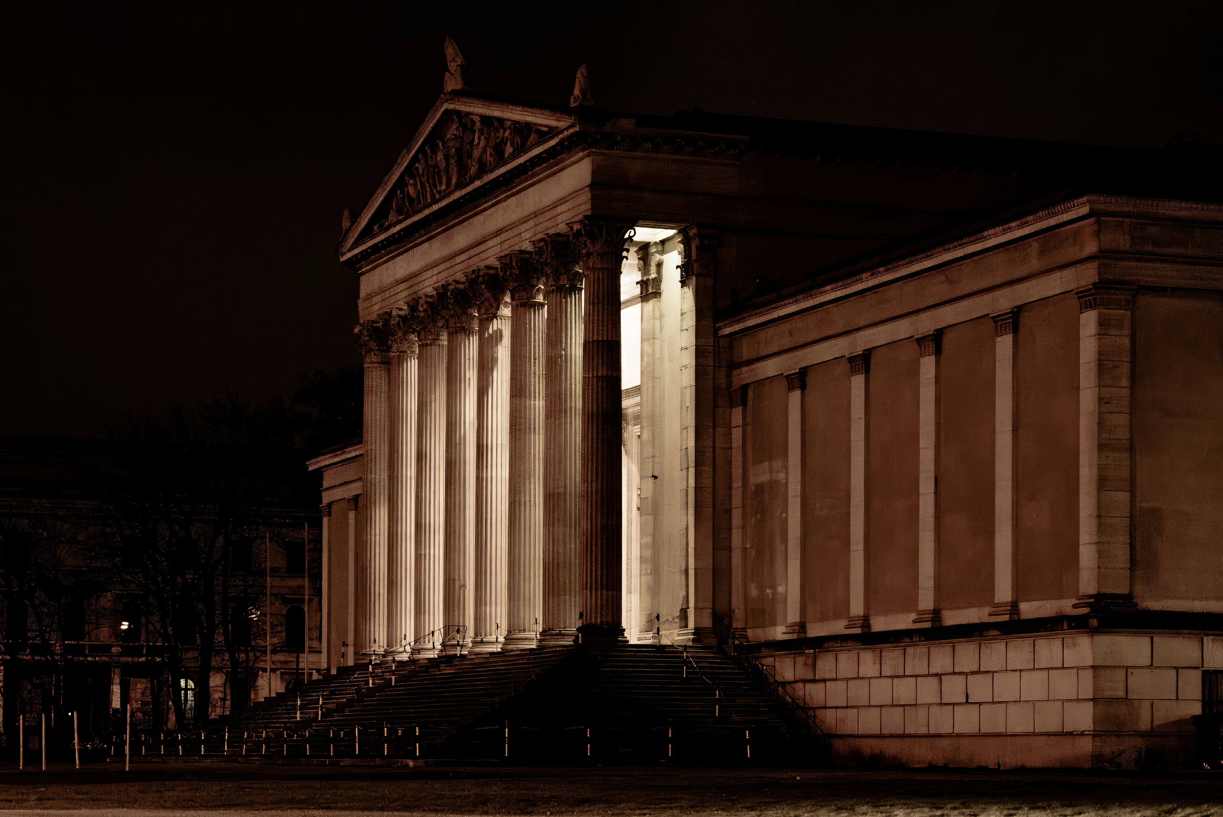 Neoclassical building with grand columns bathed in warm light against a dark backdrop.
