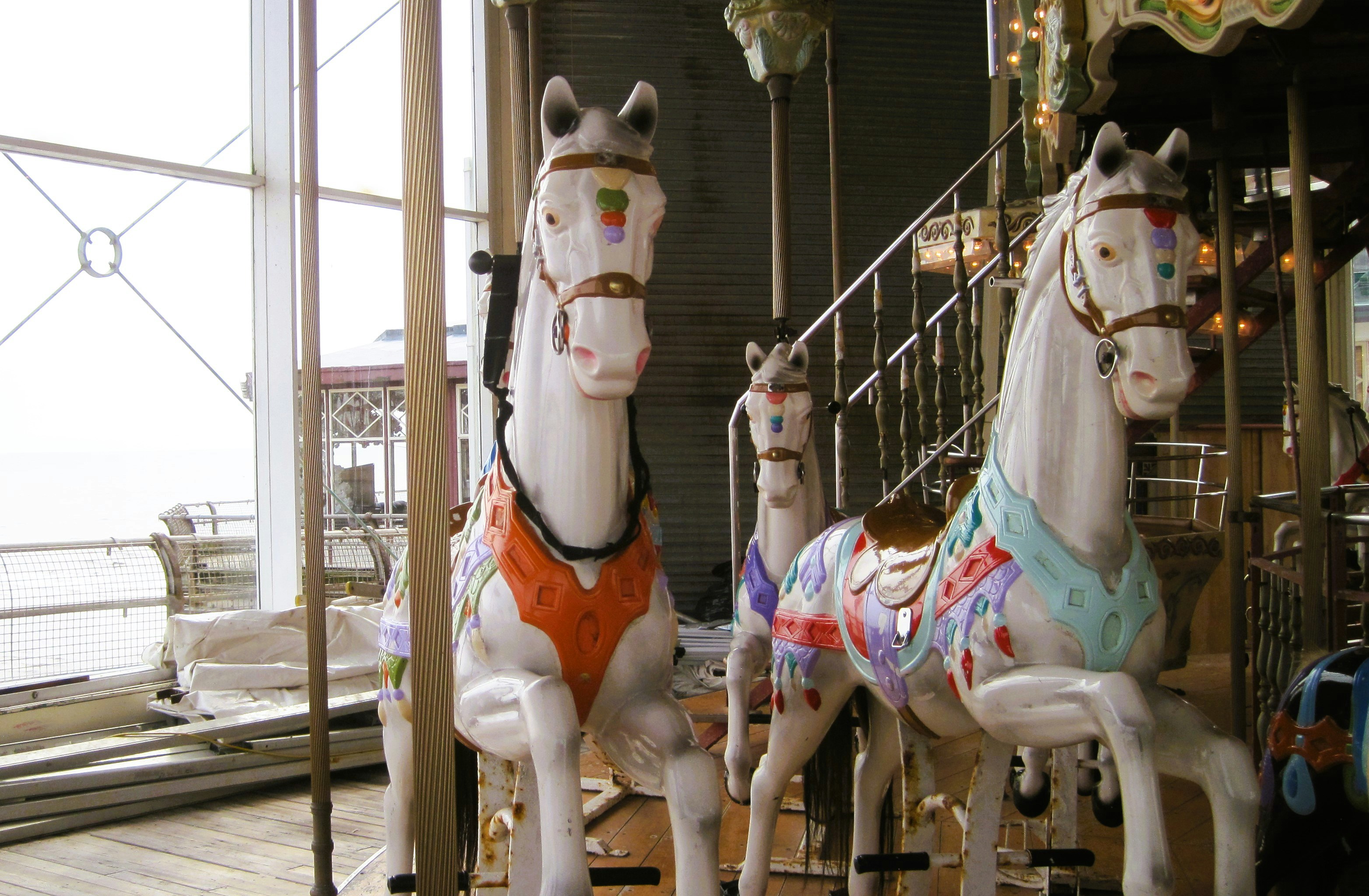 Colorful carousel horses with ornate saddles on a seaside boardwalk carousel, captured in daylight.