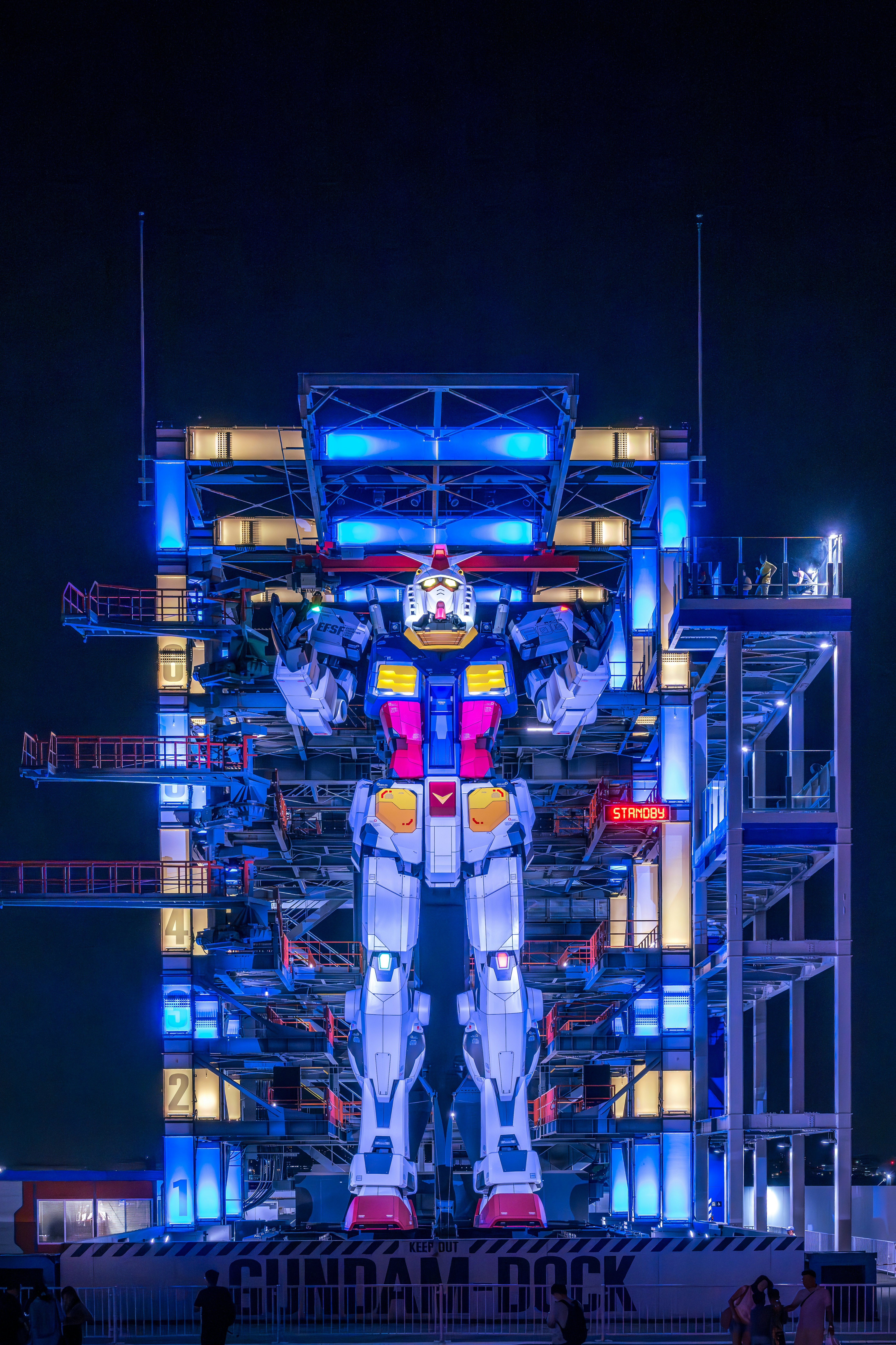 A stunning nighttime view of the life-sized Gundam robot in Yokohama, Japan, illuminated with vibrant blue and red lights. The futuristic docking station adds an industrial and sci-fi aesthetic to this iconic figure. A must-visit for anime enthusiasts and fans of Japanese pop culture.
