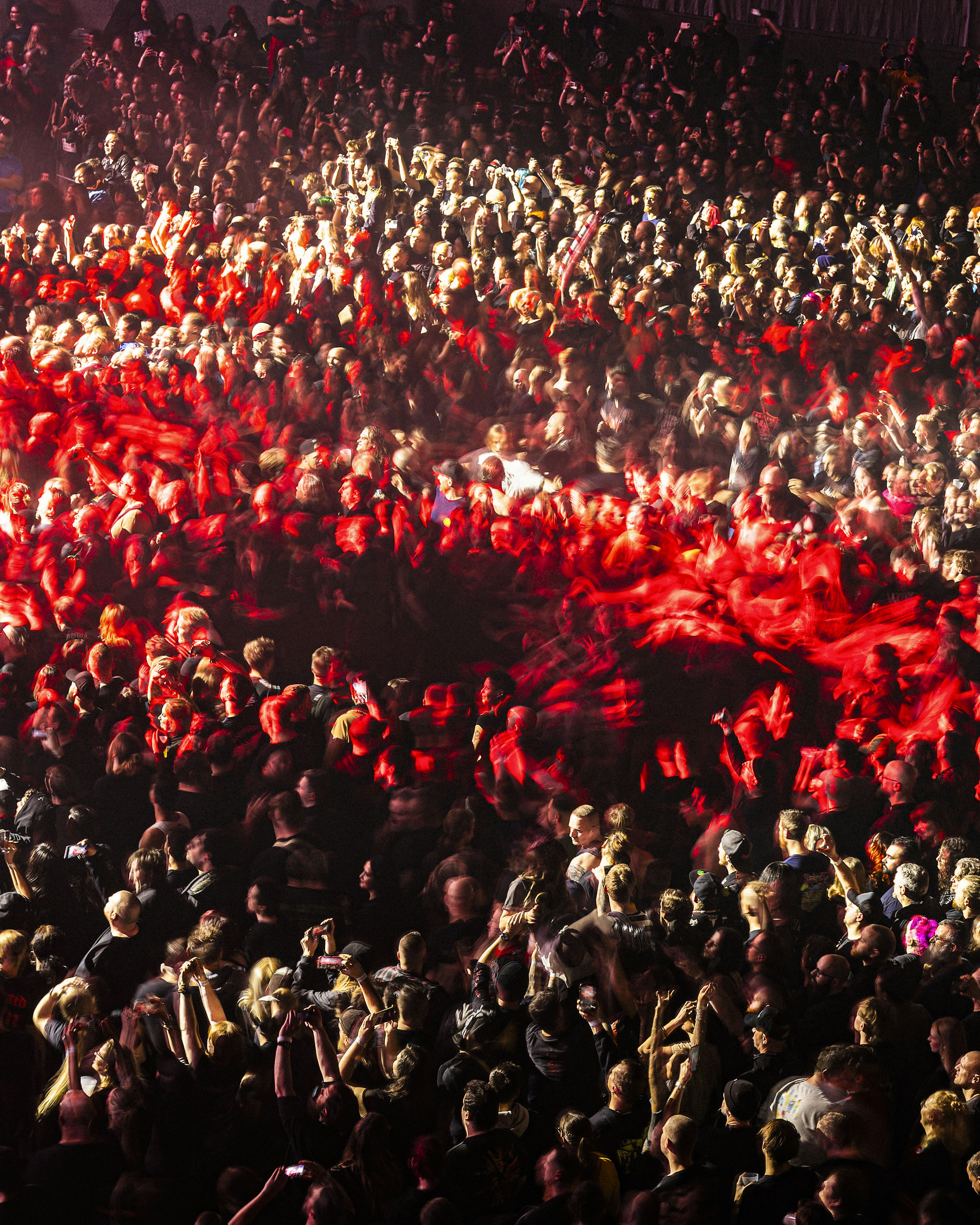 Blurred motion of a vibrant crowd illuminated by red lights at a rock concert.