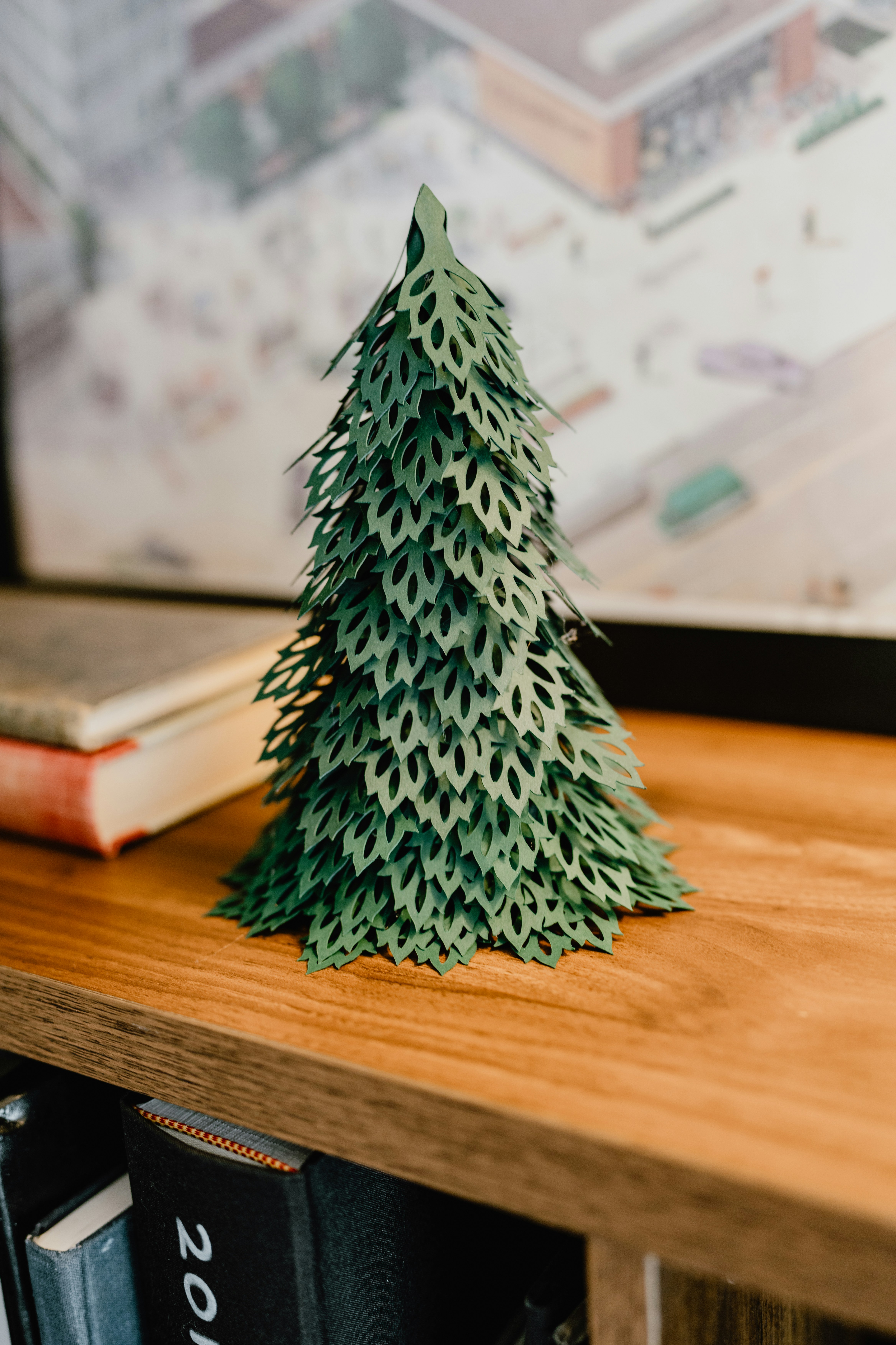 Intricate paper tree sculpture on a wooden shelf with blurred urban artwork in the background.