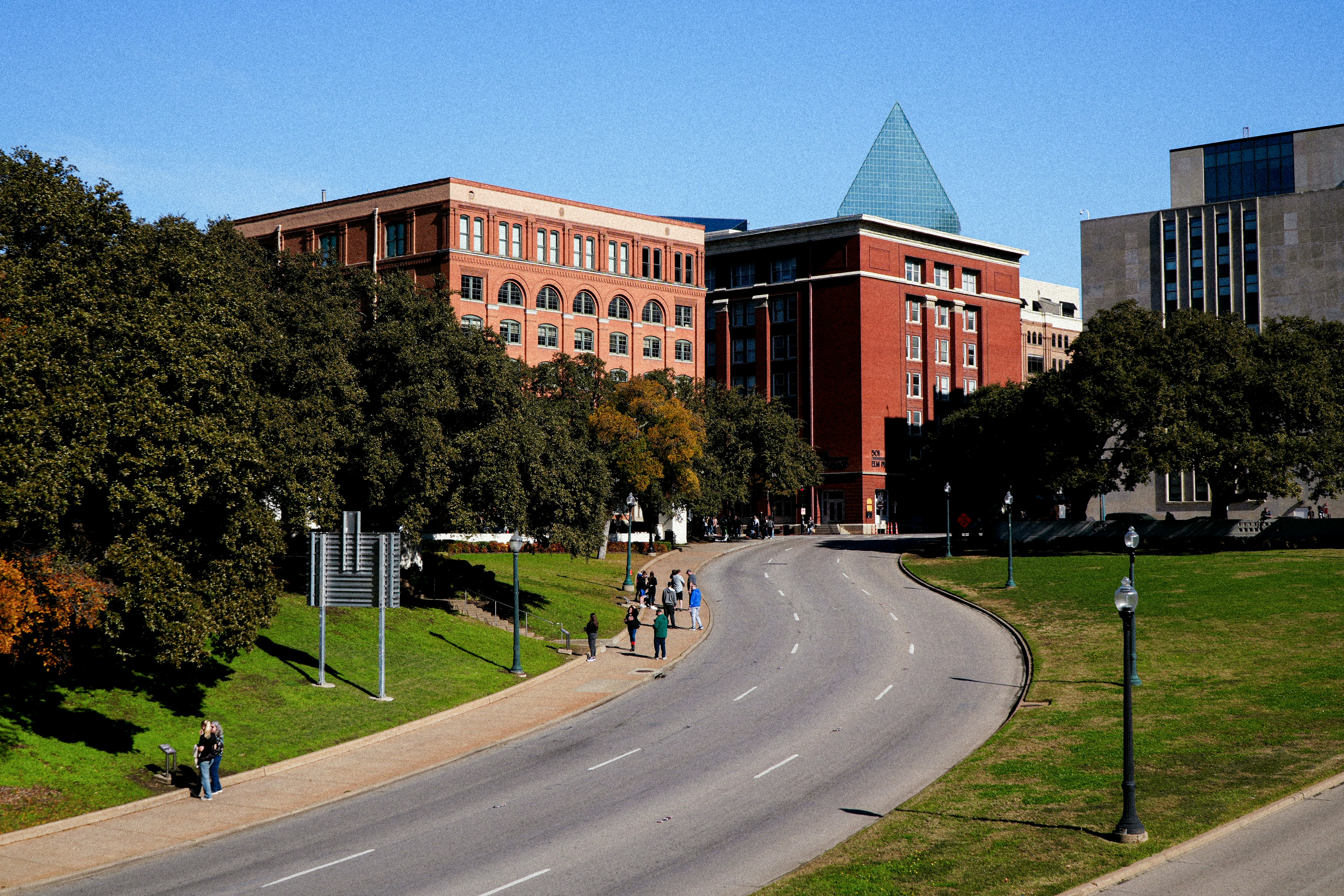 Curved road flanked by grassy slopes and historic red brick building under a clear blue sky.