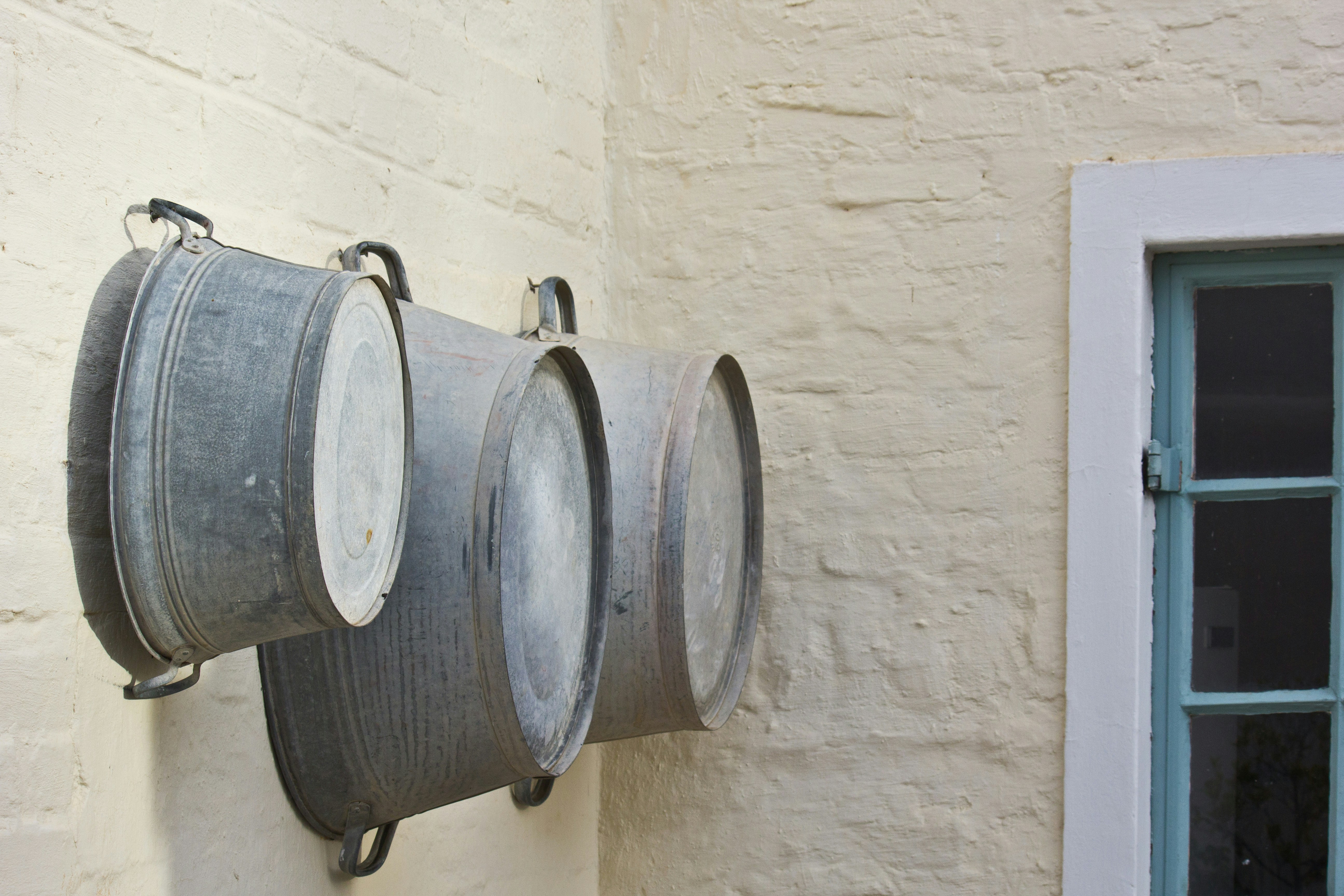 Three weathered metal basins cling to a sunlit stucco wall