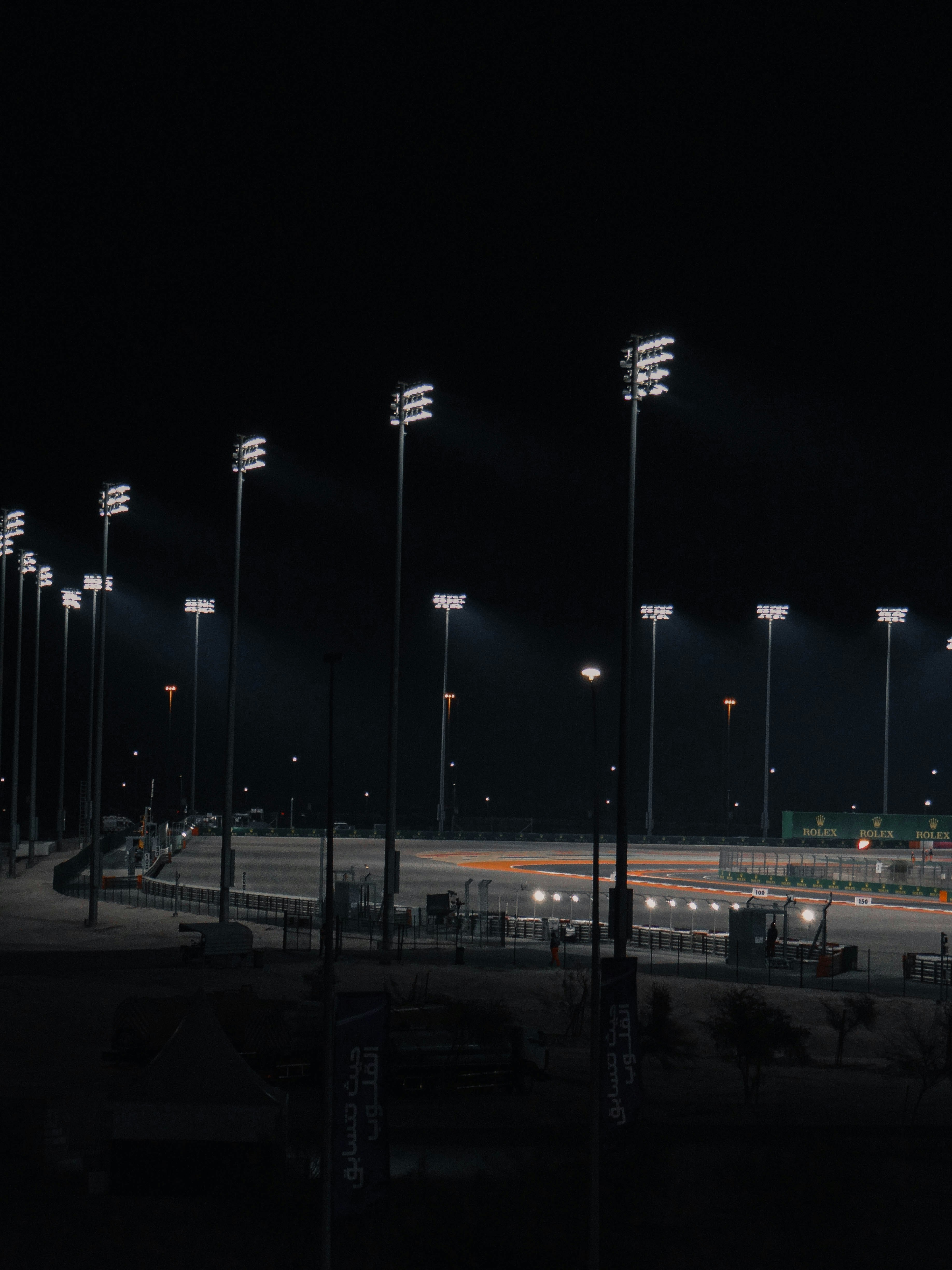 A well-lit raceway under a dark sky, featuring towering floodlights and a detailed track layout. The atmosphere suggests preparation for an exciting event.
