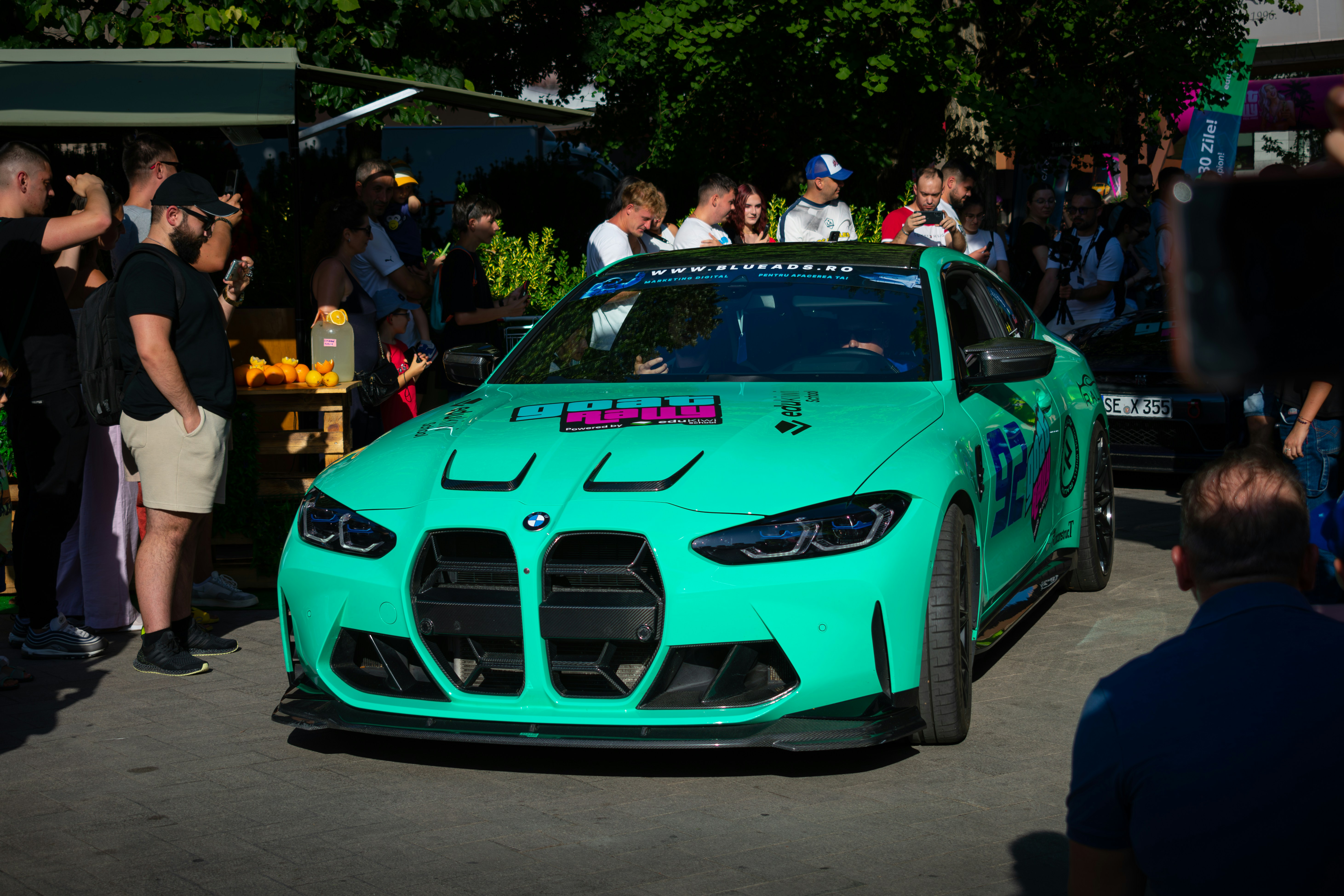 Teal sports car surrounded by spectators in an outdoor setting.