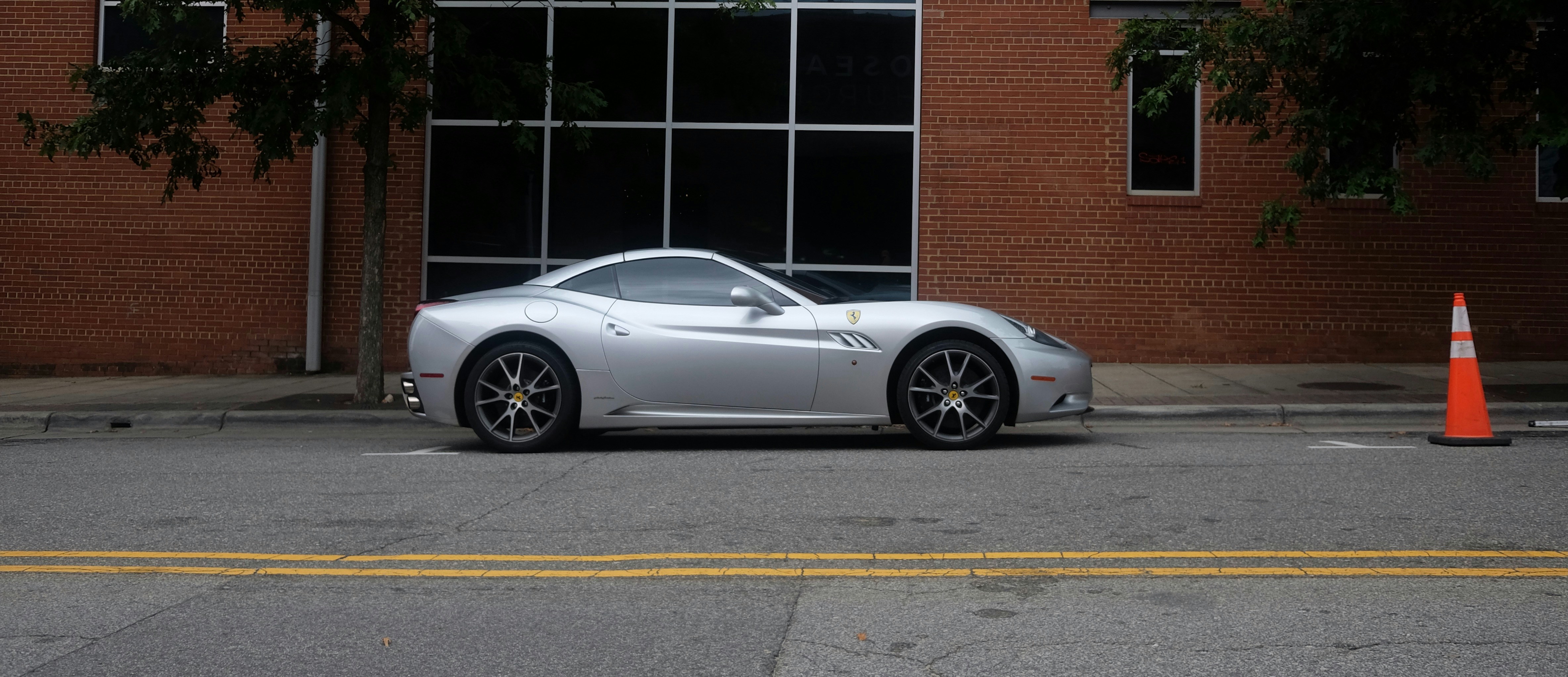 Sleek silver sports car parked beside a brick building with a traffic cone nearby on an empty street.