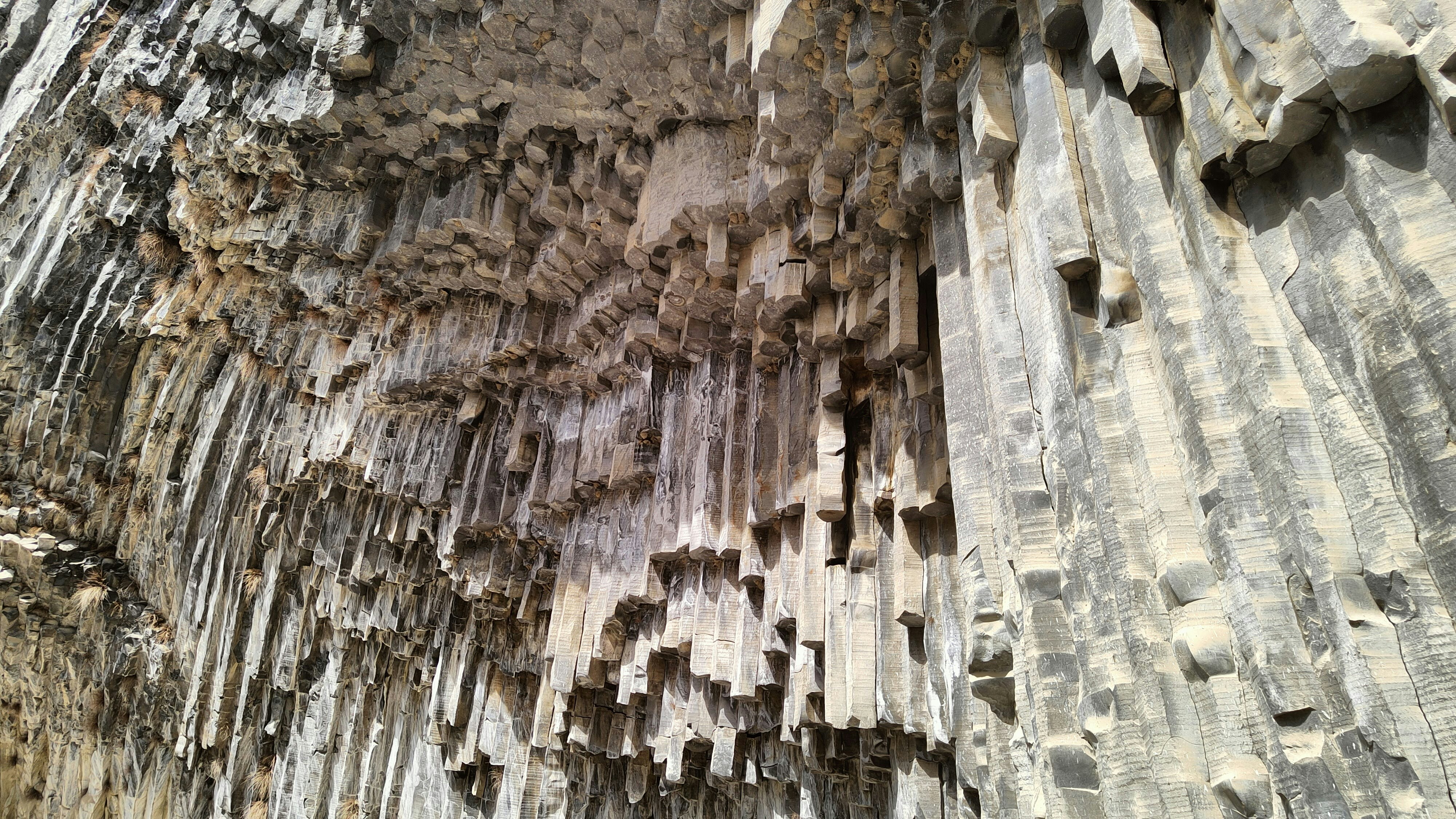 Close-up photograph of basalt columnar joints forming a ribbed cliff face with geometric stone patterns.