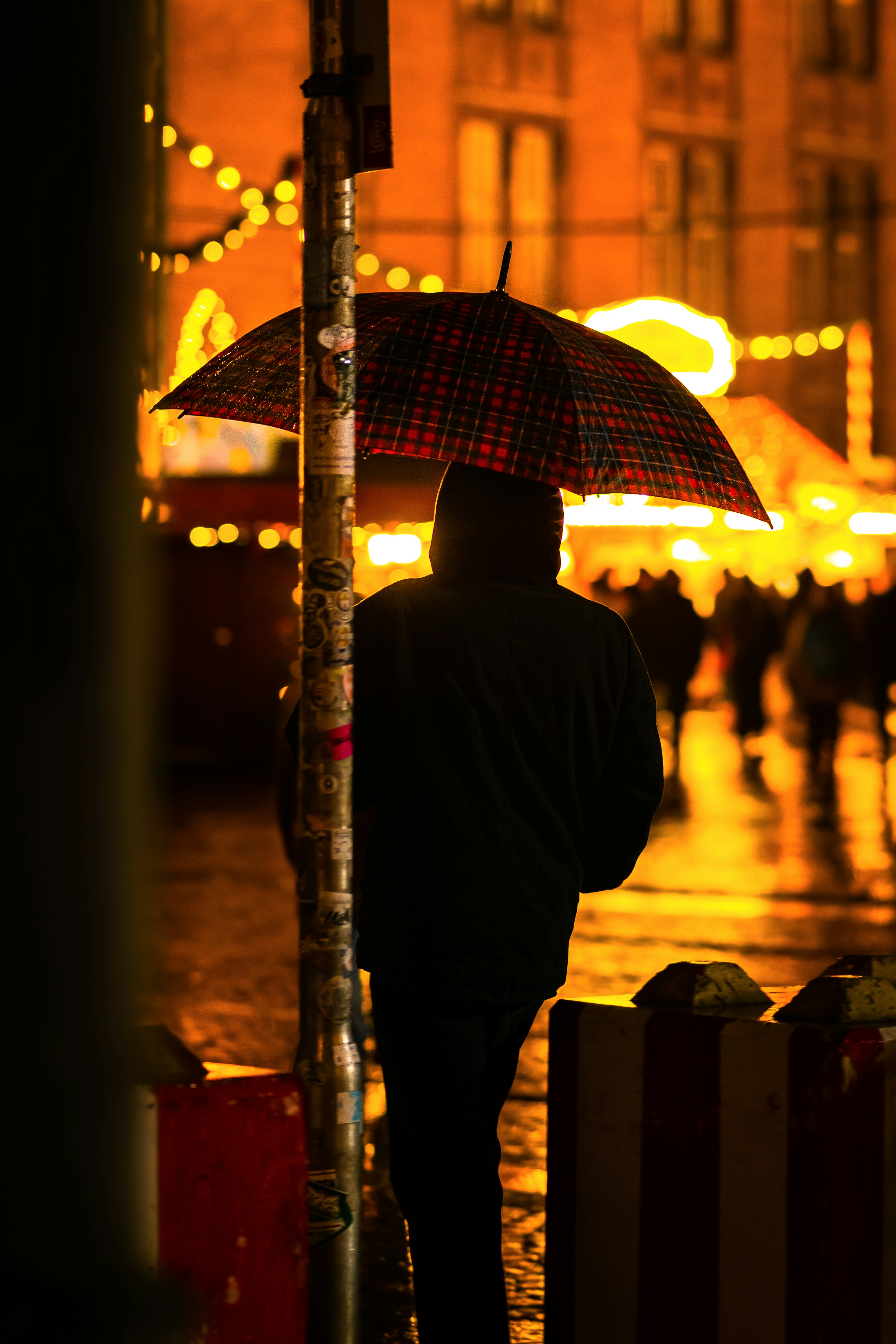 Plaid Umbrella in Neon Rain: A Quiet Figure Traversing a Warm-Glow Street