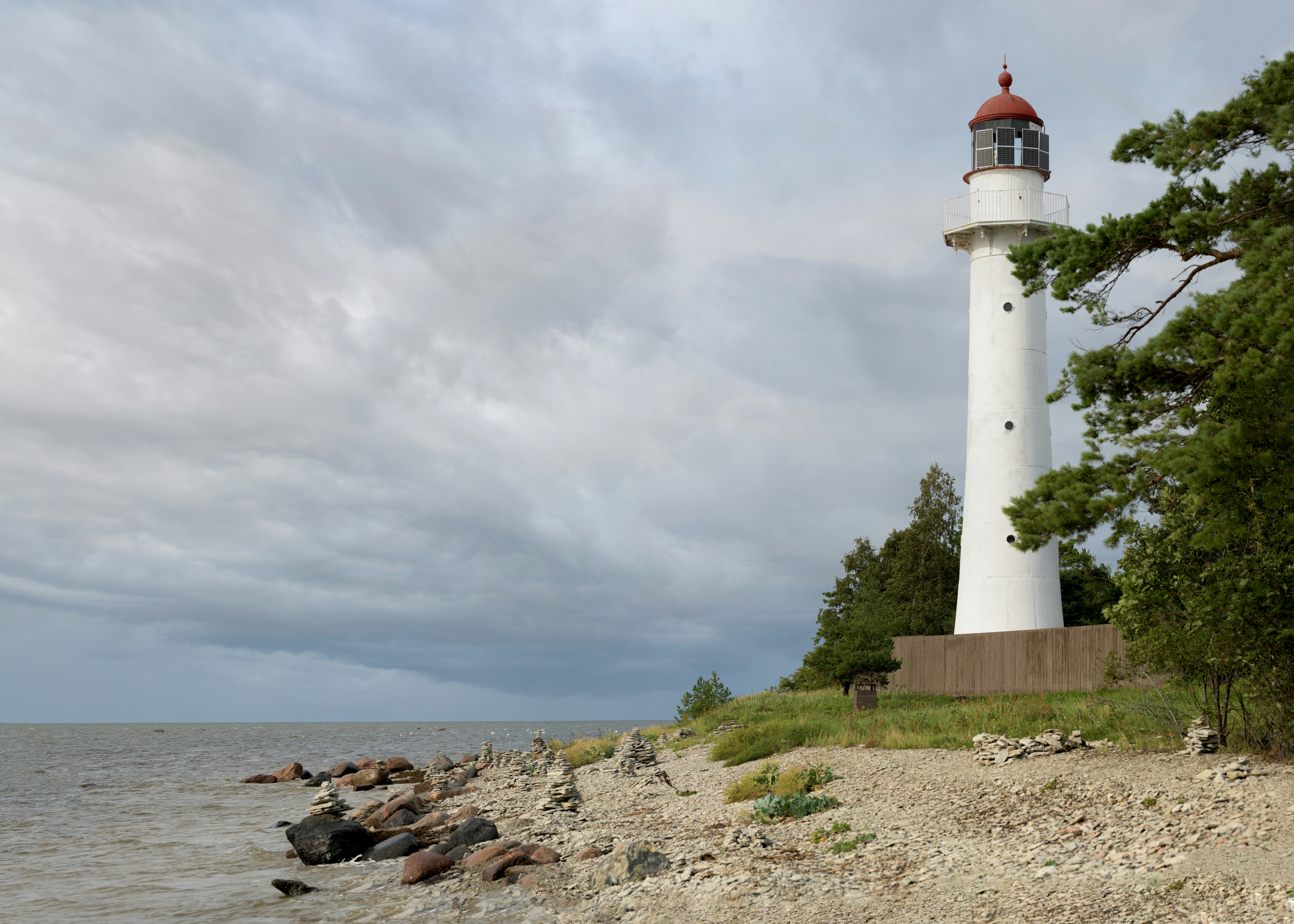 The Lighthouse Guard: White Beacon on a Pebble Coast Under Cloudy Skies