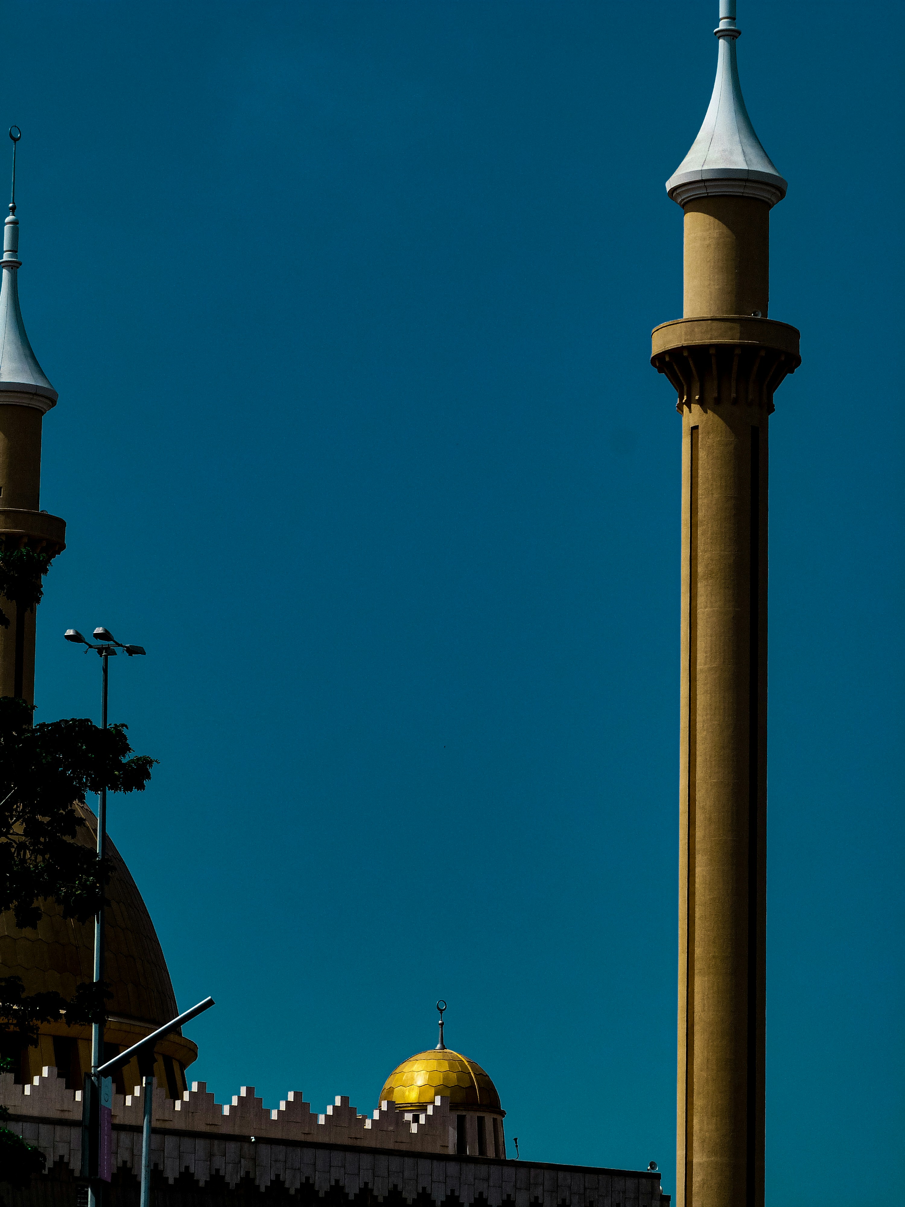 Golden dome anchors the composition as slender minarets frame a vivid blue sky, highlighting the mosque’s architectural details. This photograph emphasizes the clean lines and contrast between the warm stone and the deep blue backdrop.